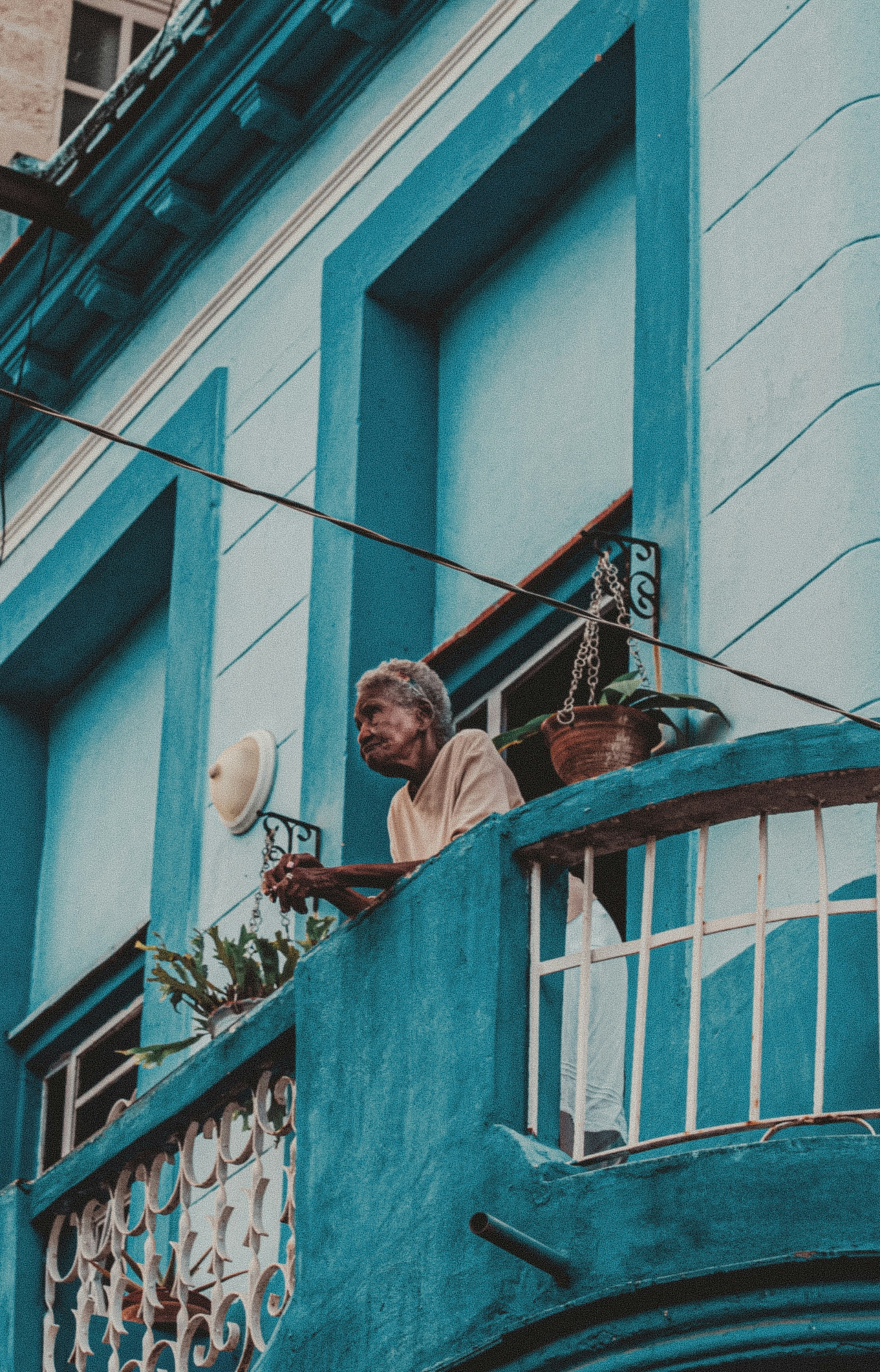 Blue Veranda Gaze: A weathered figure on a turquoise balcony