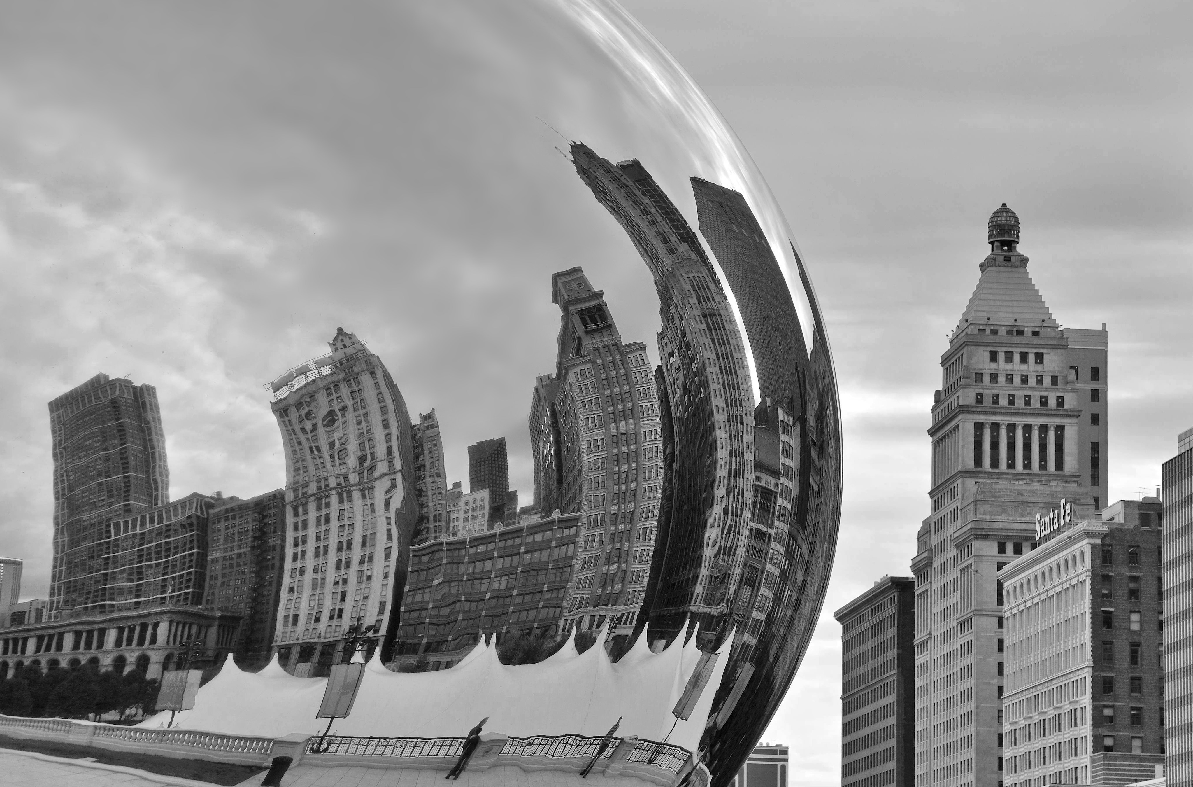 Grayscale cityscape with skyscrapers reflected in a large, curved metallic surface.