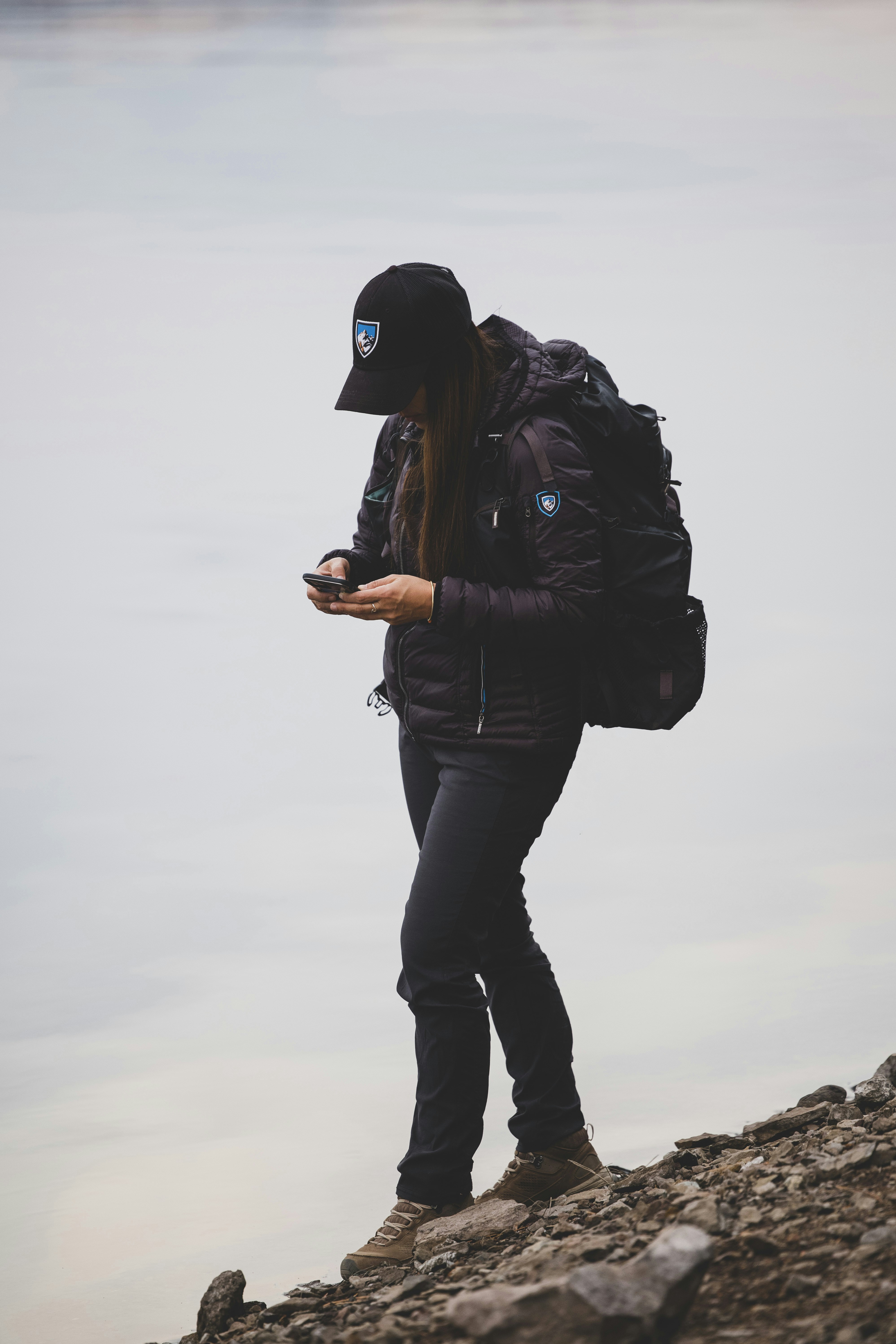 Traveler in Shadowed Jacket Taps a Quiet Moment Along the Shore
