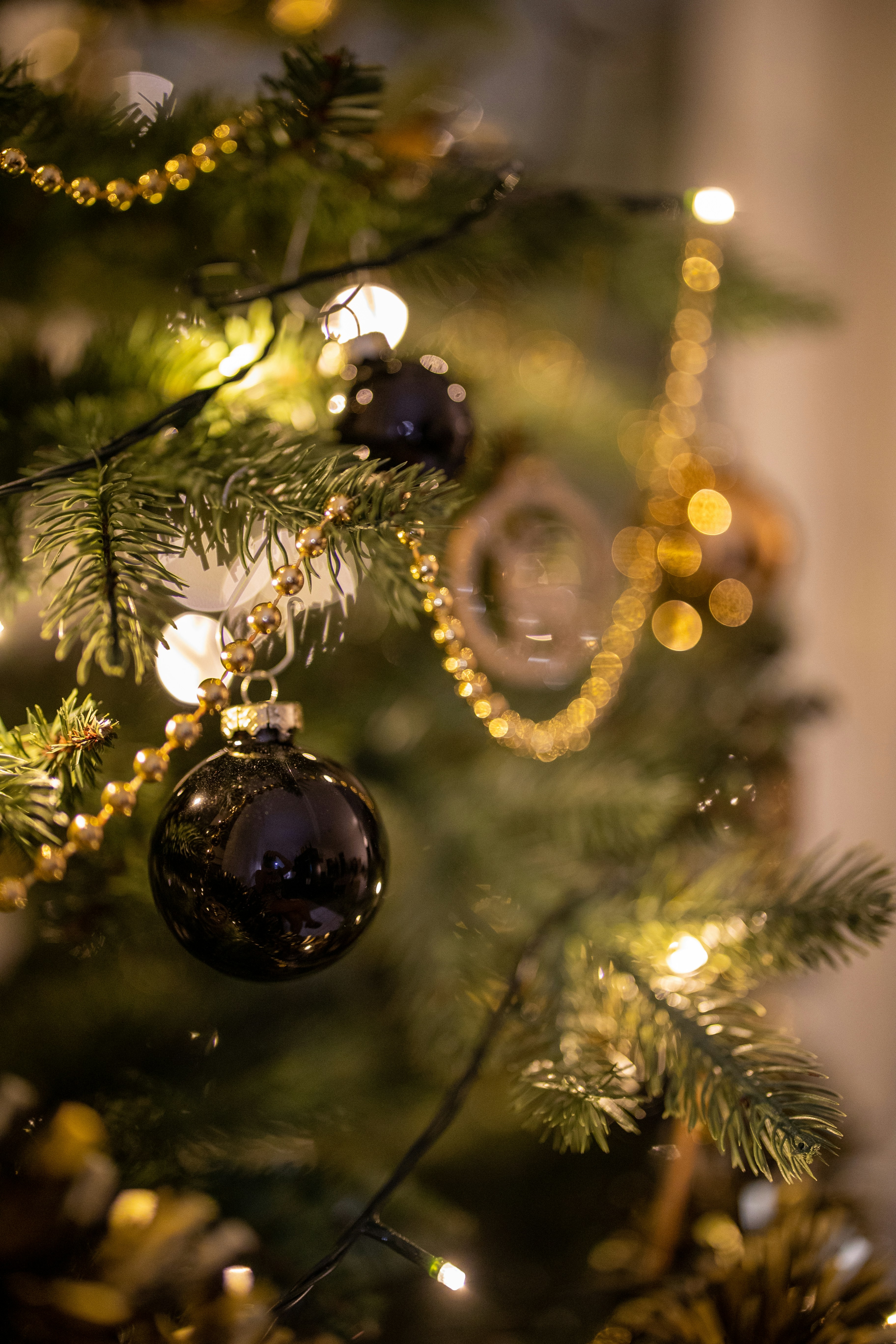 Black ornament hanging from a Christmas tree, surrounded by twinkling lights and golden garlands.
