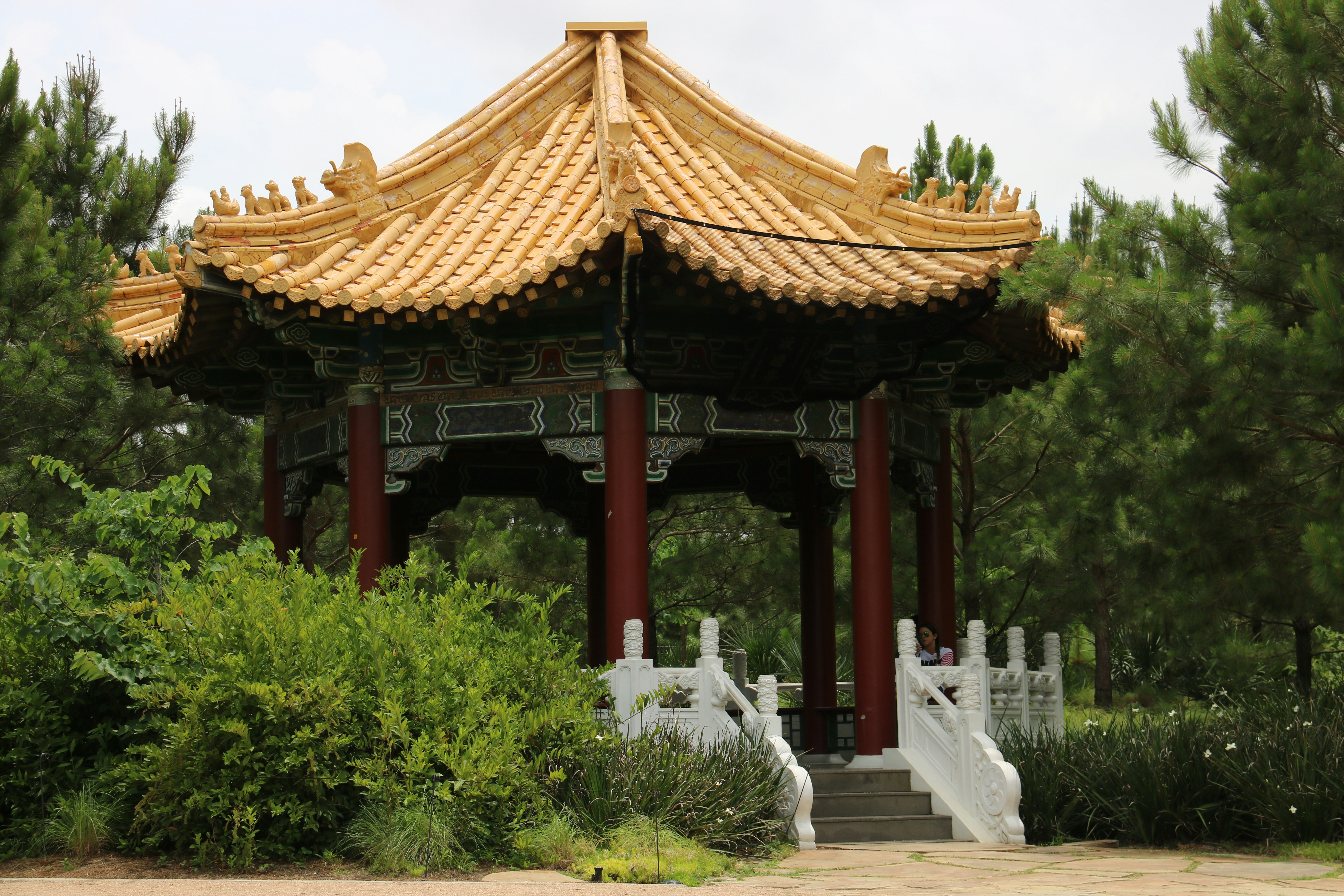 Traditional Asian gazebo surrounded by lush greenery, showcasing intricate roof details and elegant columns.