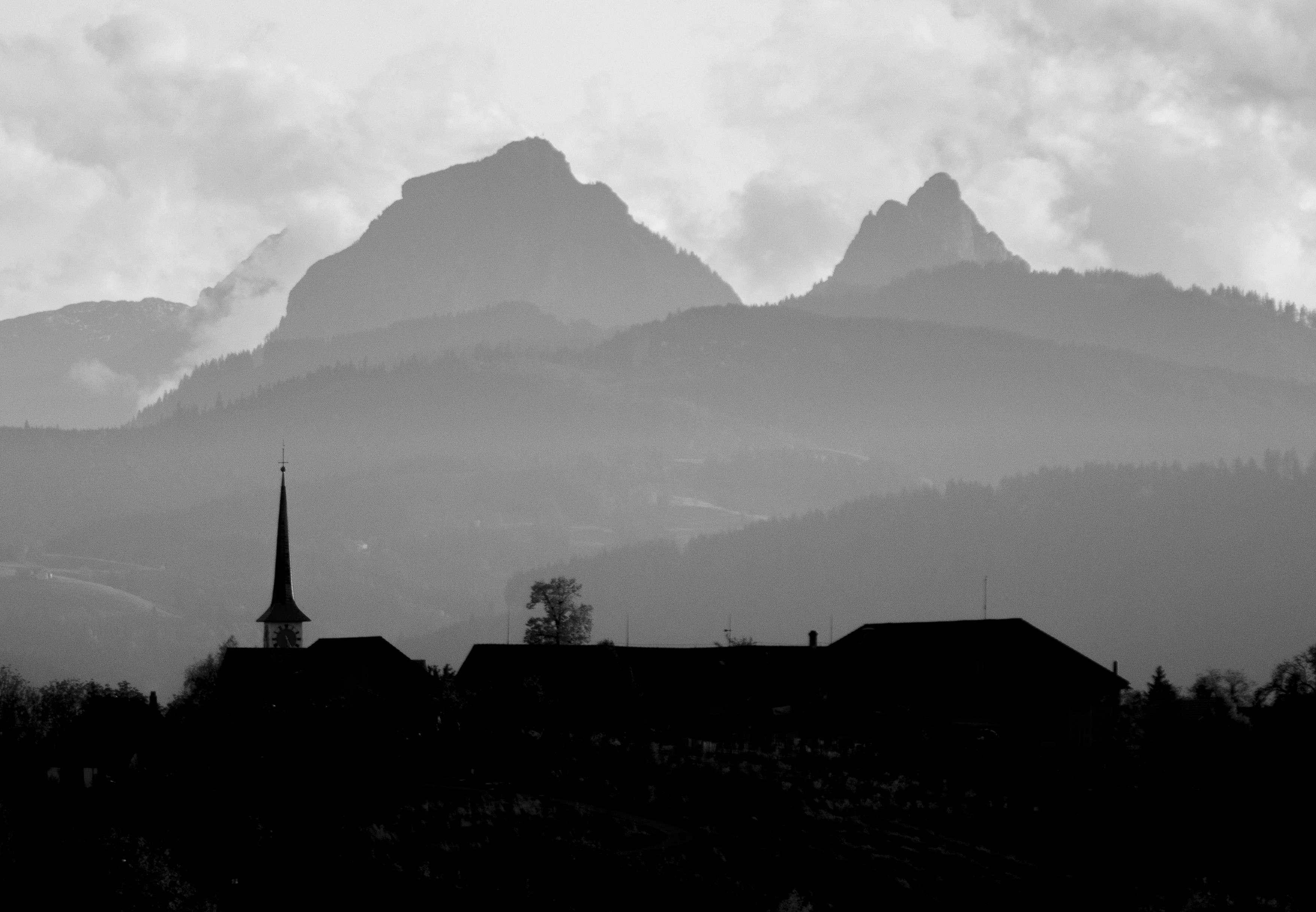 A serene landscape featuring a silhouetted church steeple against a backdrop of misty mountains. The monochromatic tones enhance the tranquil atmosphere.