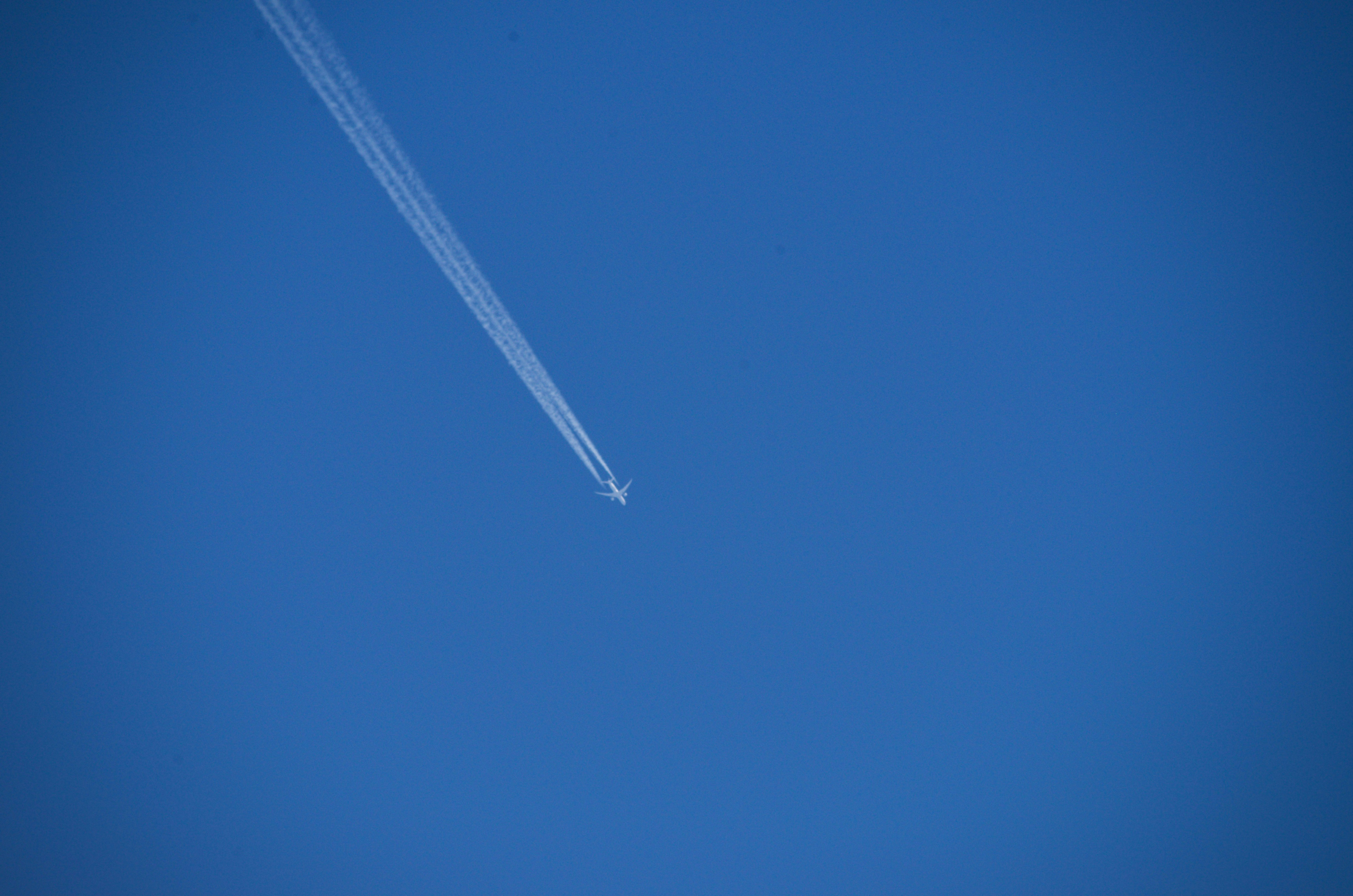 A high-flying aircraft leaves a trail of vapor against a clear blue sky, illustrating the intersection of human ingenuity and nature's expanse.