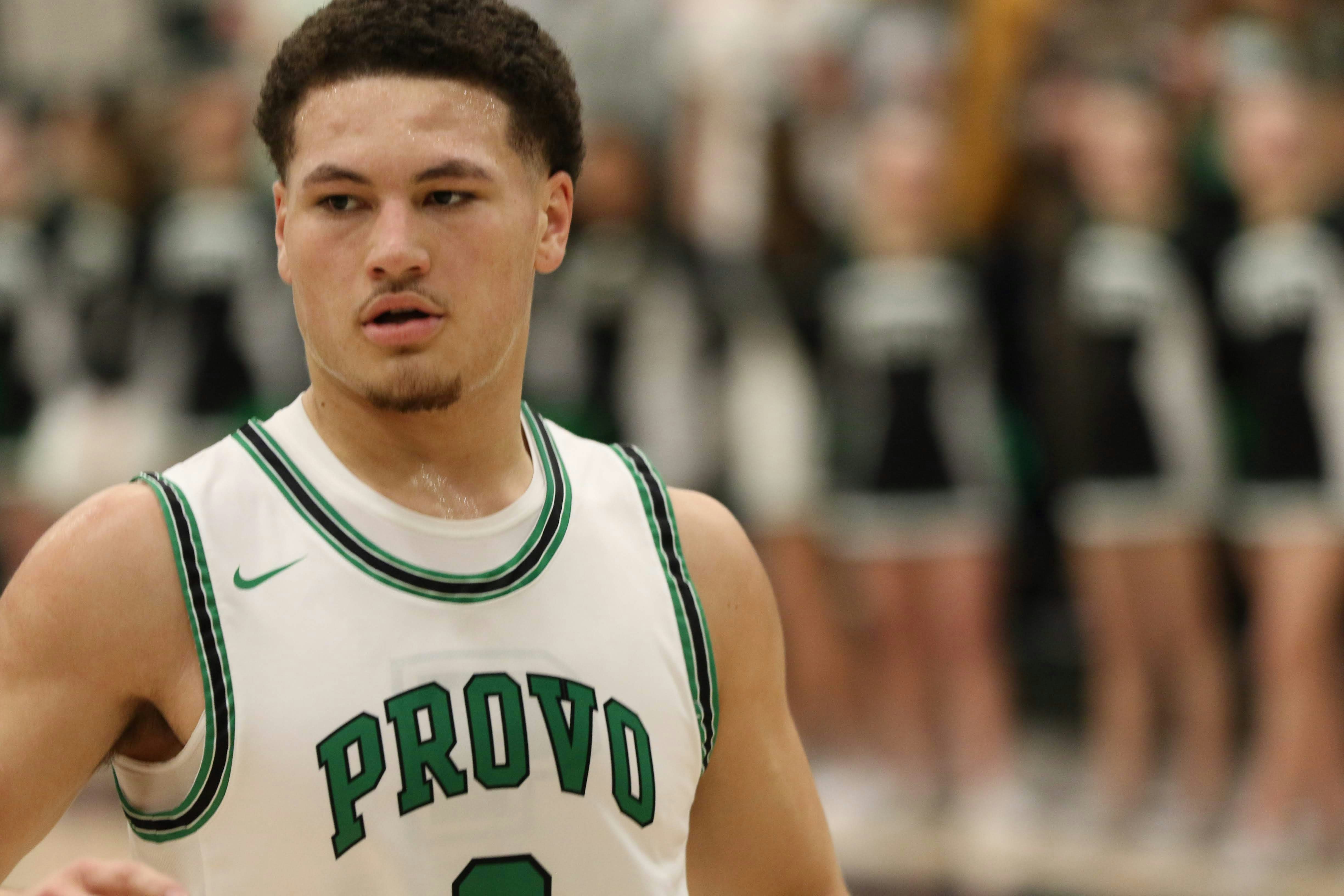 Basketball player in Provo jersey with cheerleaders blurred in the background.