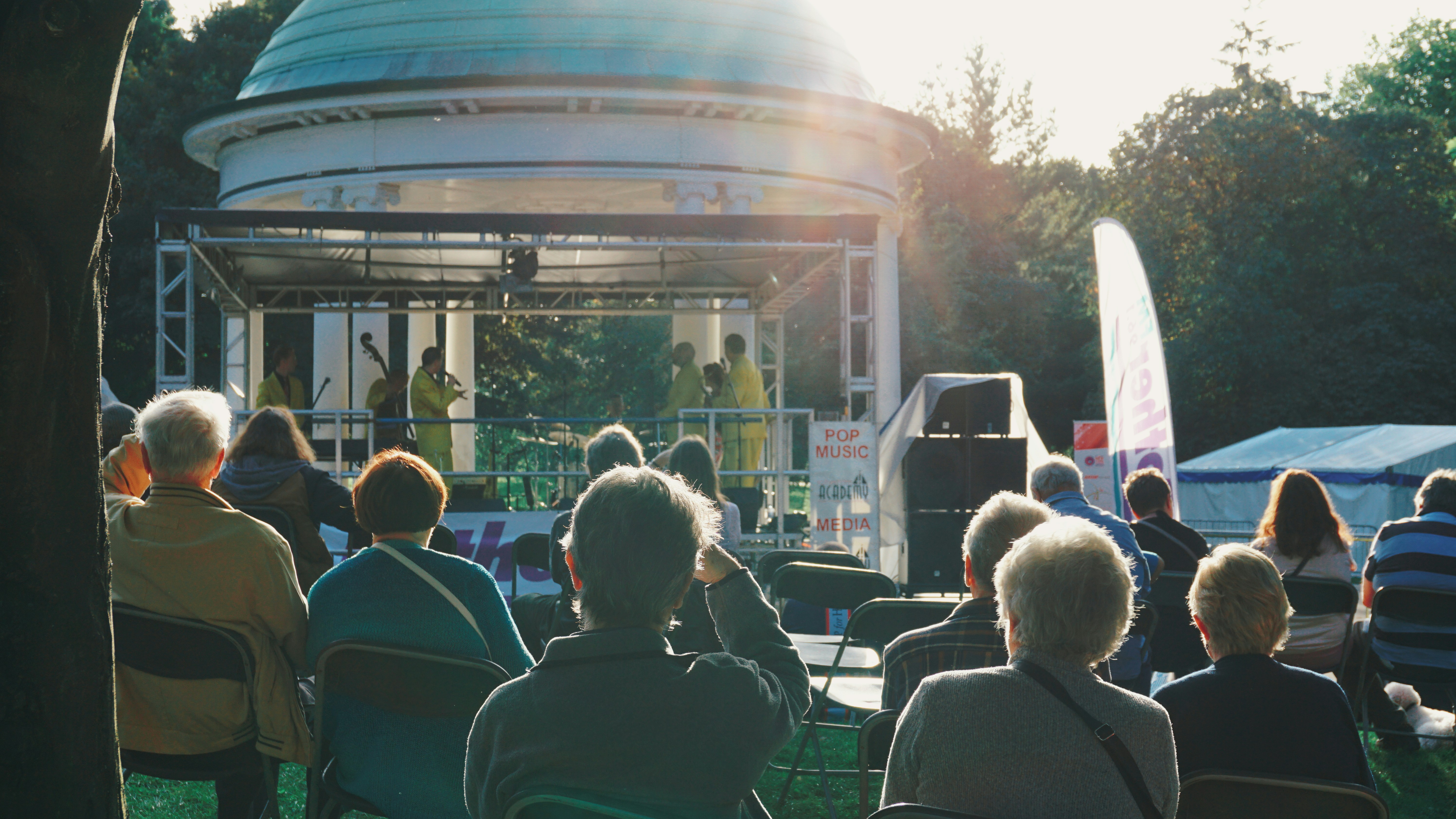 People seated outdoors facing a white bus under a sunny sky.