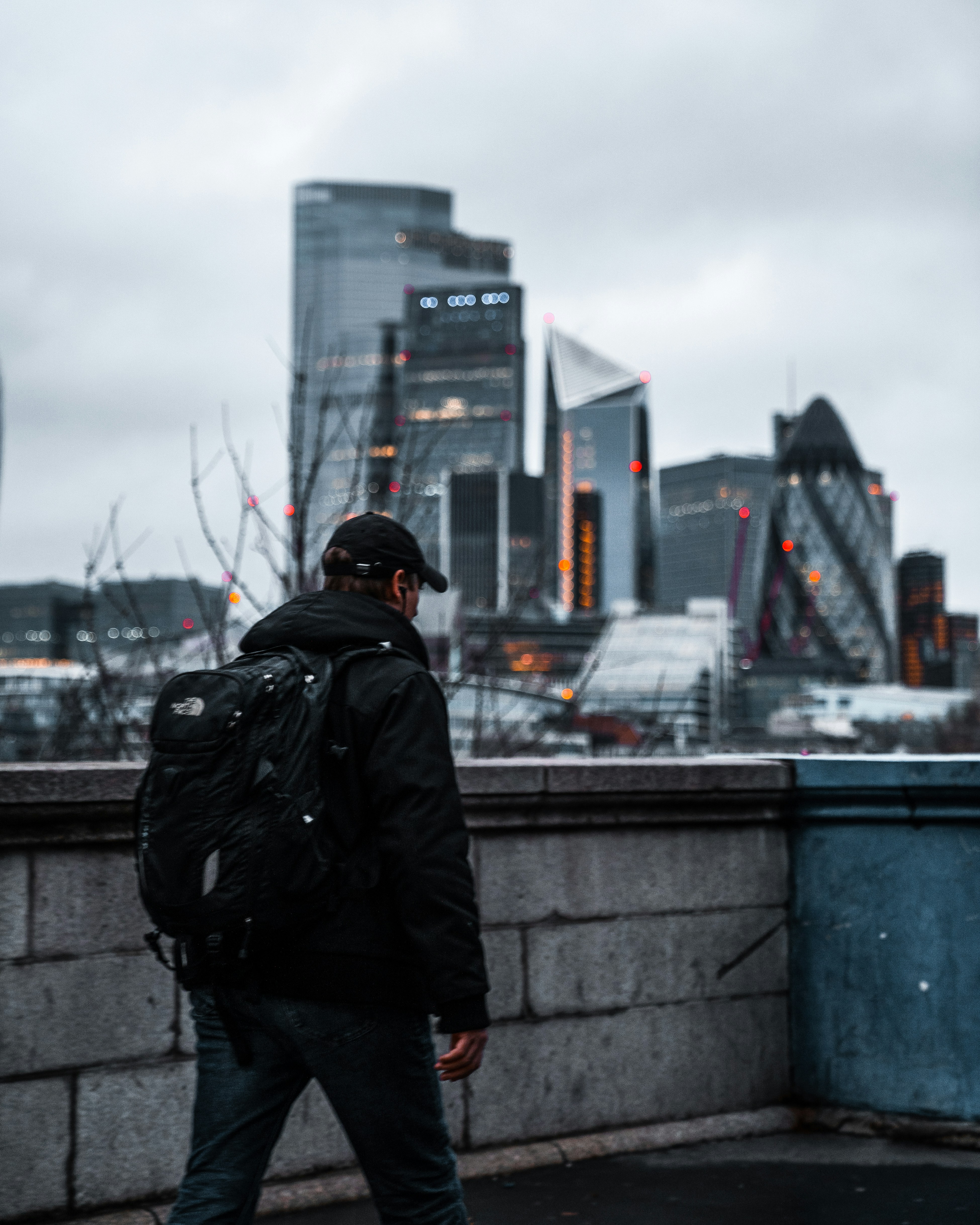 On the Railing, Toward the Towers: A Lone Wanderer by the City Skyline