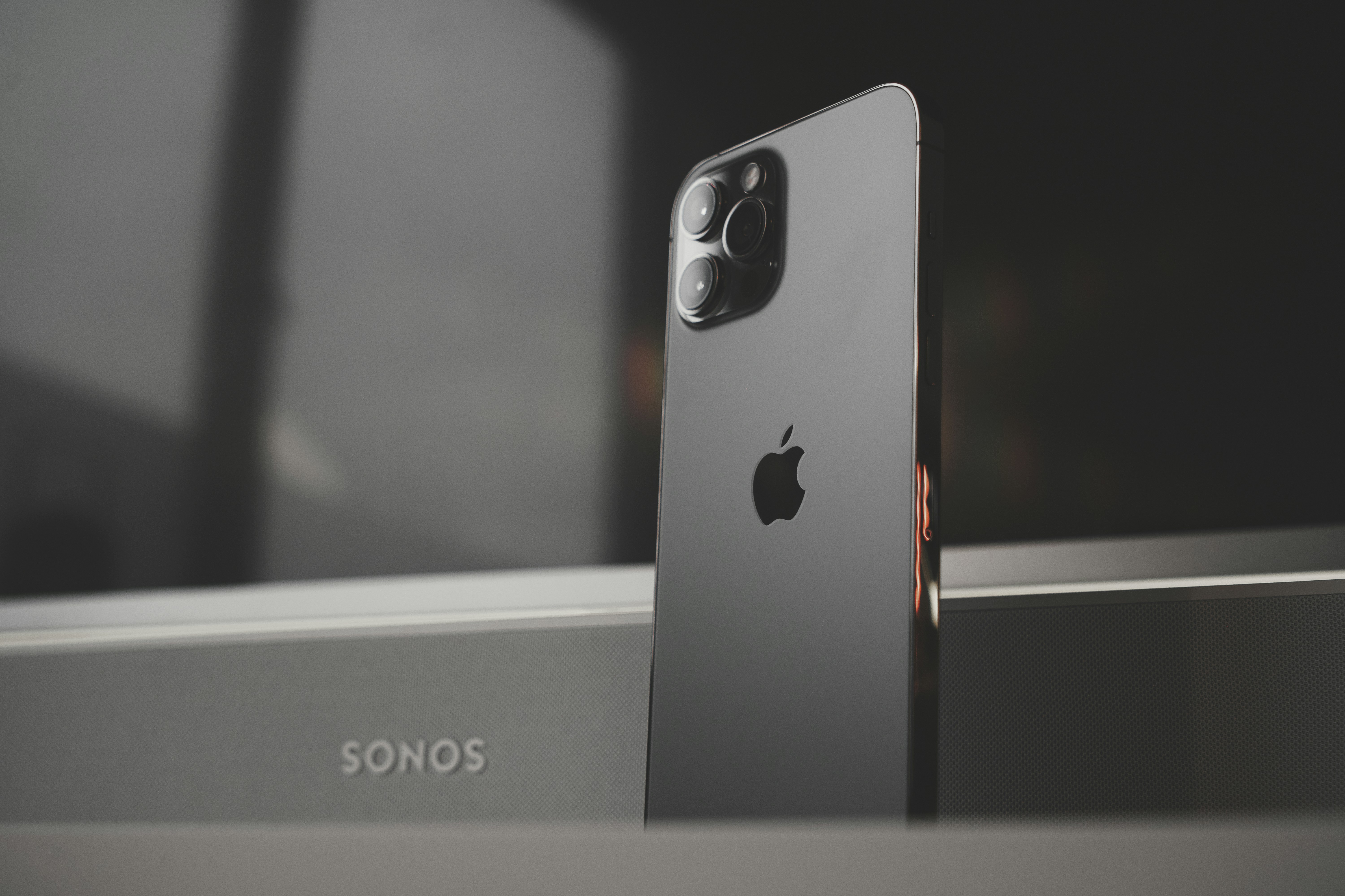 Sleek black Apple smartphone positioned against a Sonos speaker, showcasing modern design elements. The scene captures a blend of technology and minimalism.