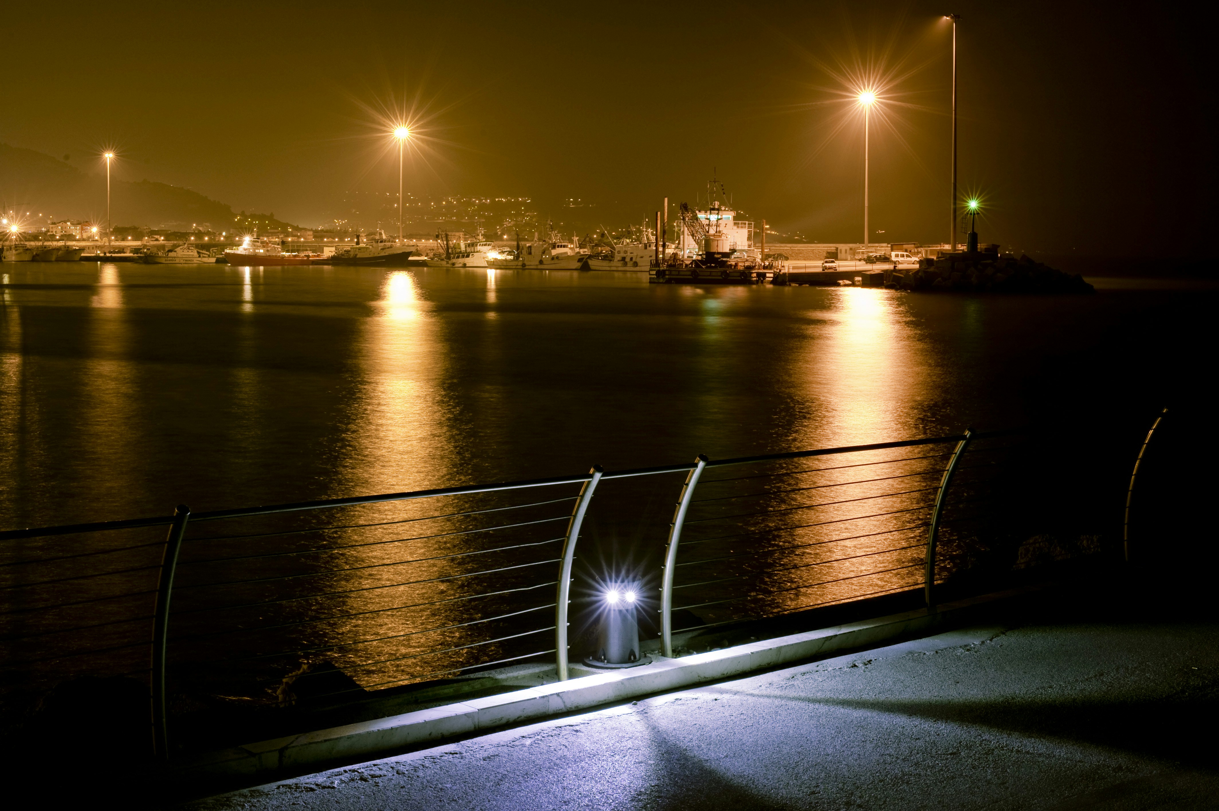 Illuminated harbor scene at night, showcasing boats and mooring lights reflecting on calm waters.