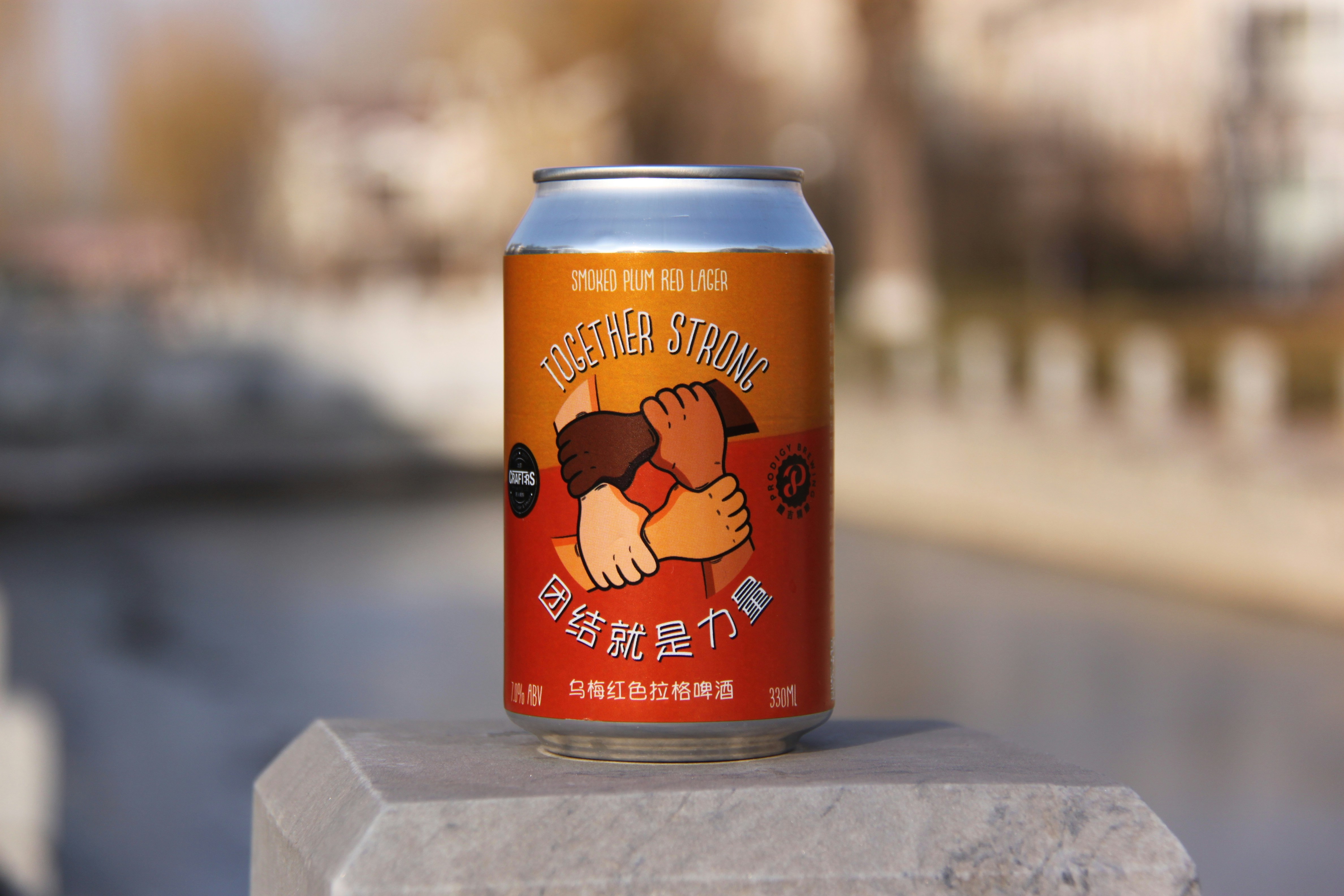 A vibrant beer can featuring intertwined hands, symbolizing strength and unity, set against a blurred urban backdrop.