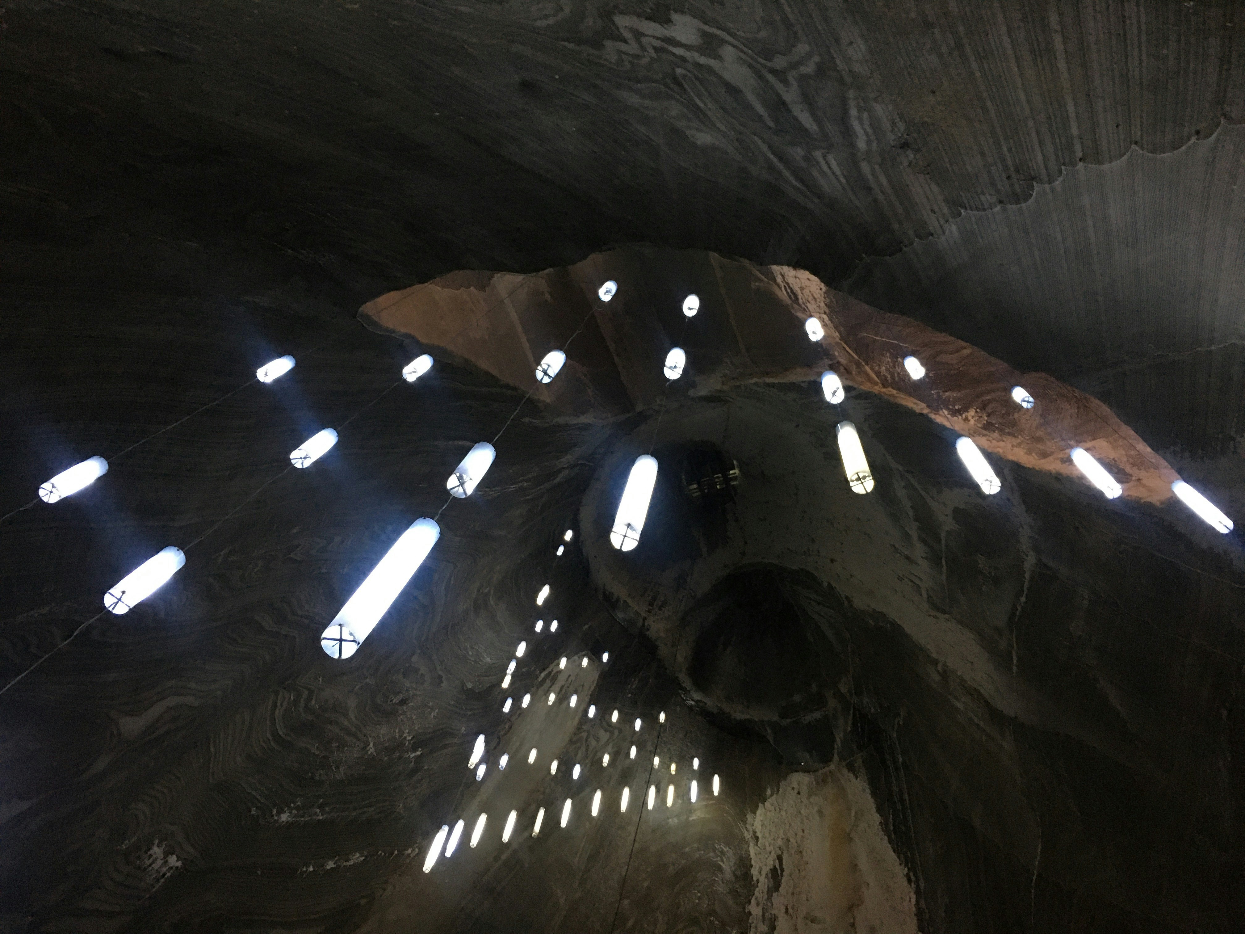 Interior of a cavern featuring elongated openings that allow beams of light to pierce through, creating a striking visual contrast against the rocky walls.