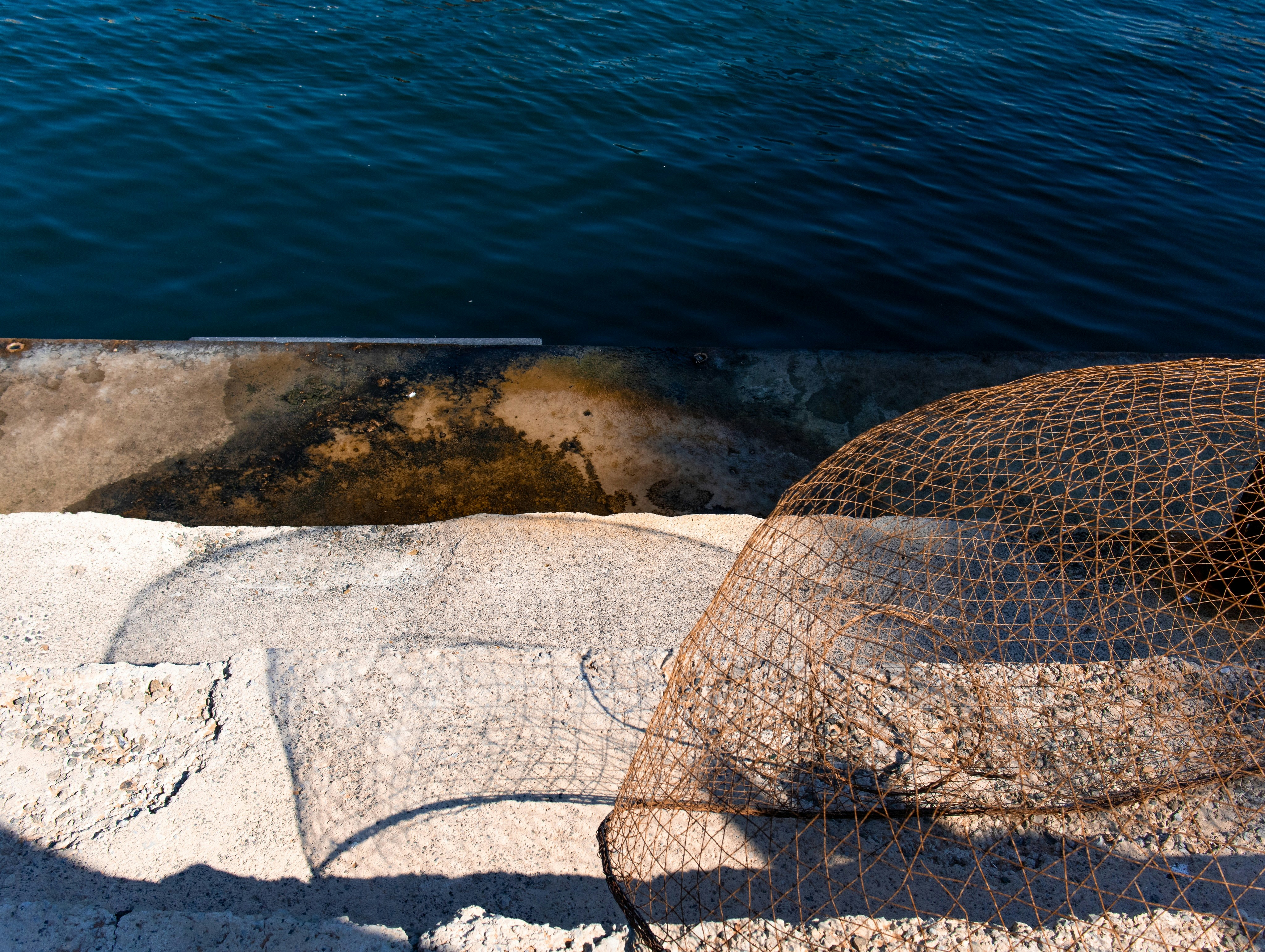 Rusted Mesh by the Pier: Geometry, Shadow, and Sea