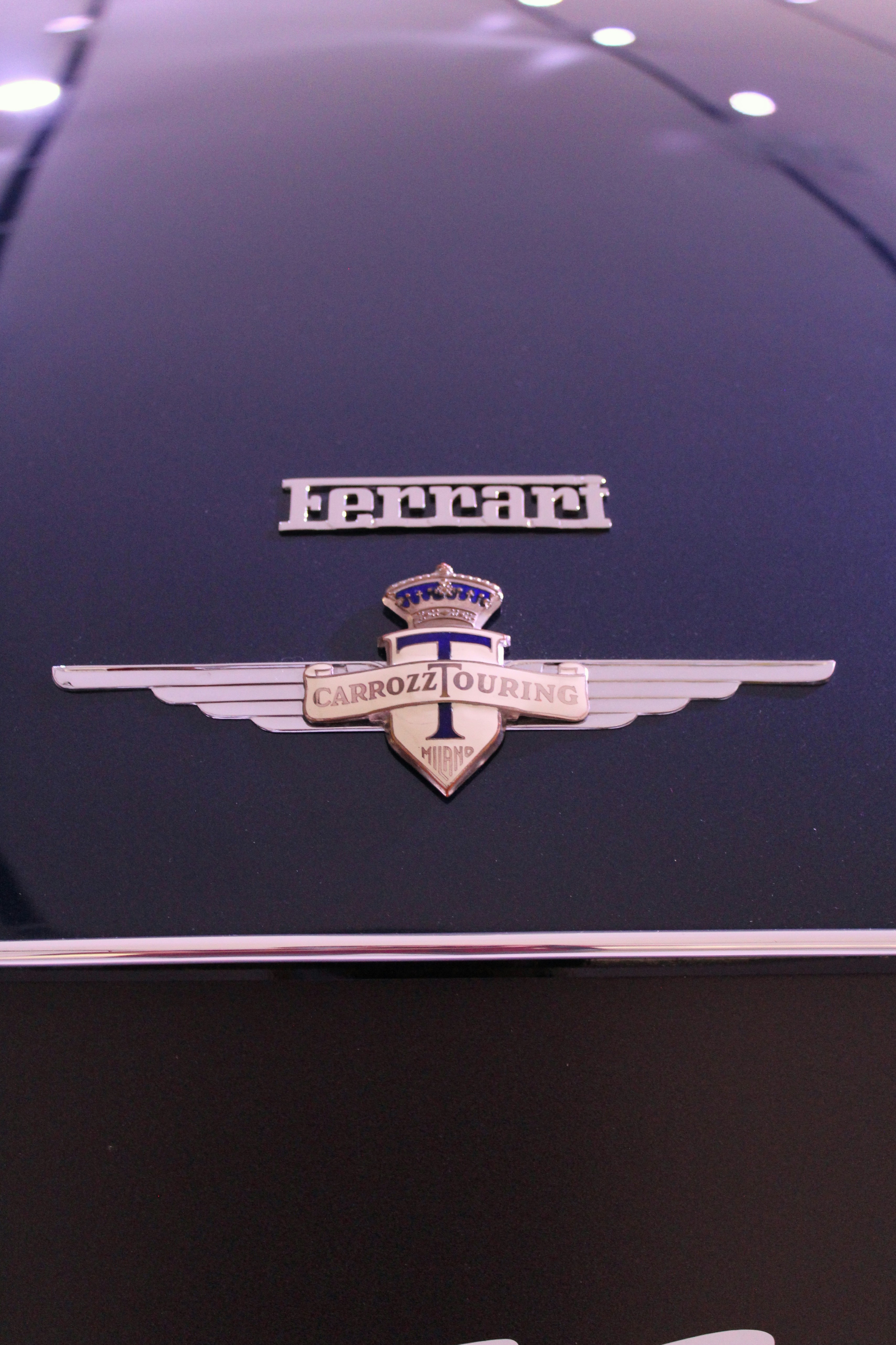 Close-up of the Ferrari logo and Carrozzeria Touring badge on a sleek black surface, showcasing automotive craftsmanship.