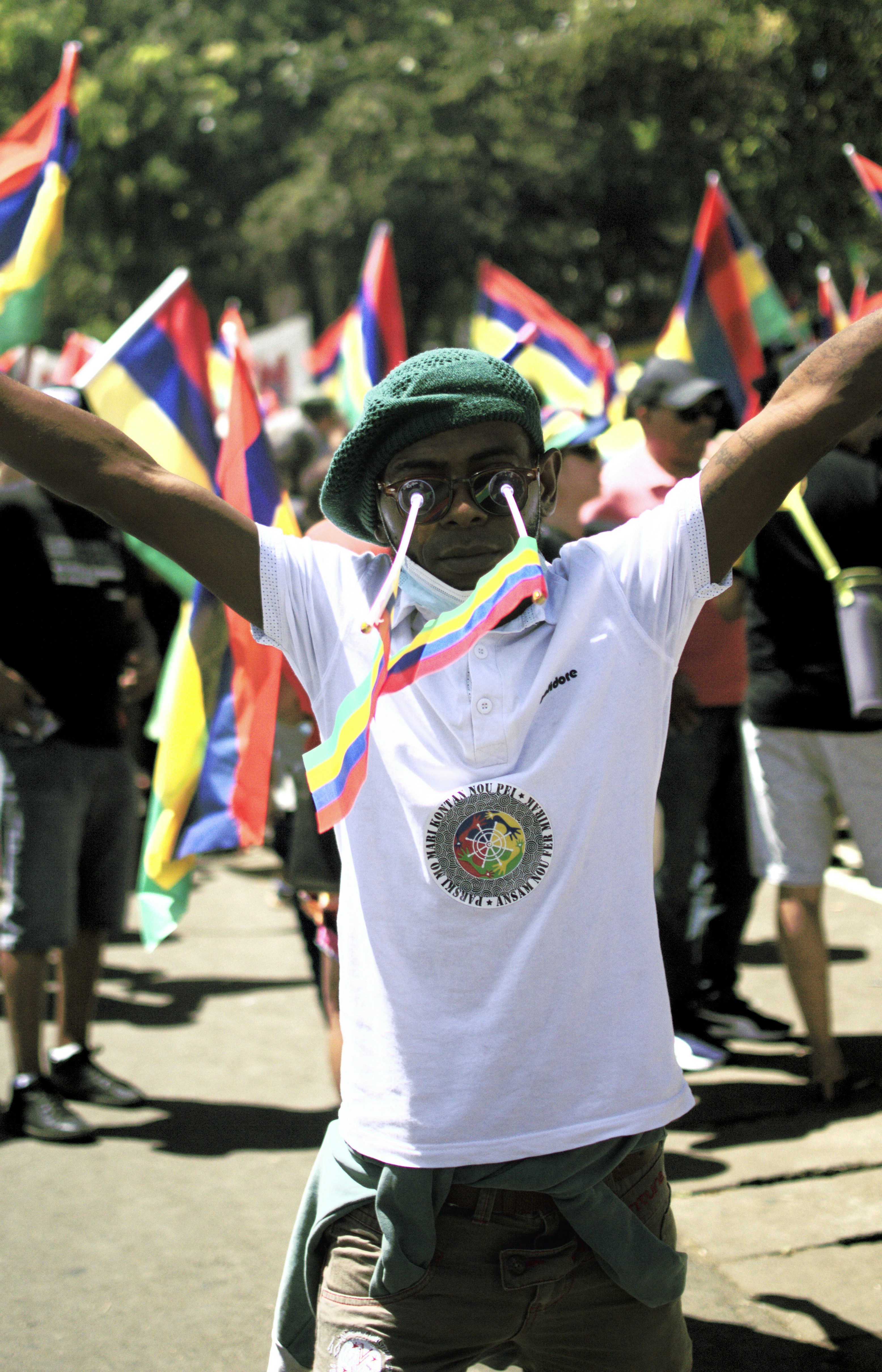 A joyful participant in a parade, proudly displaying vibrant flags while wearing sunglasses and a green beret. The scene is filled with energy and a sense of community.