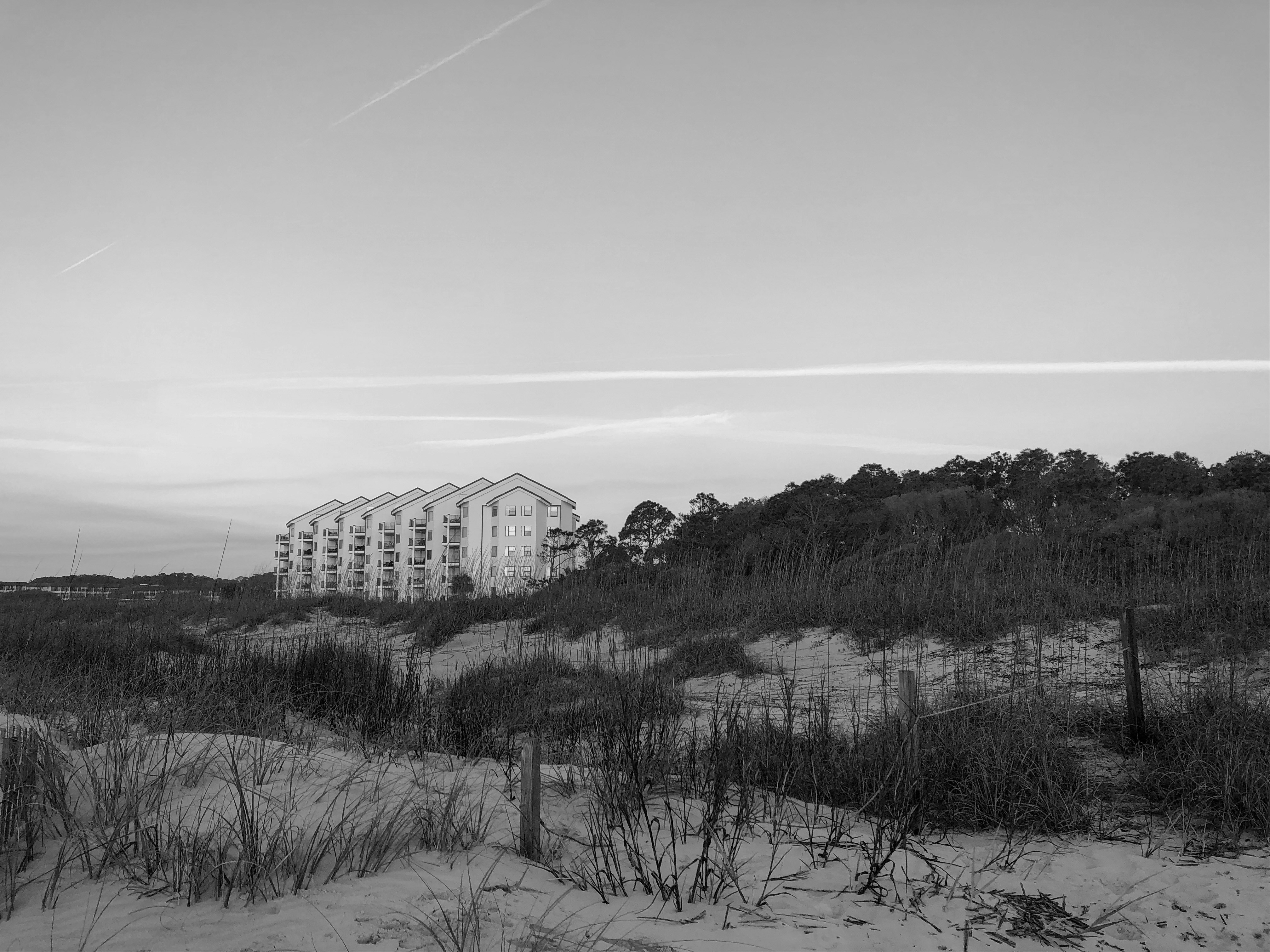 Grayscale view of a solitary building near coastal dunes with a backdrop of open sky.