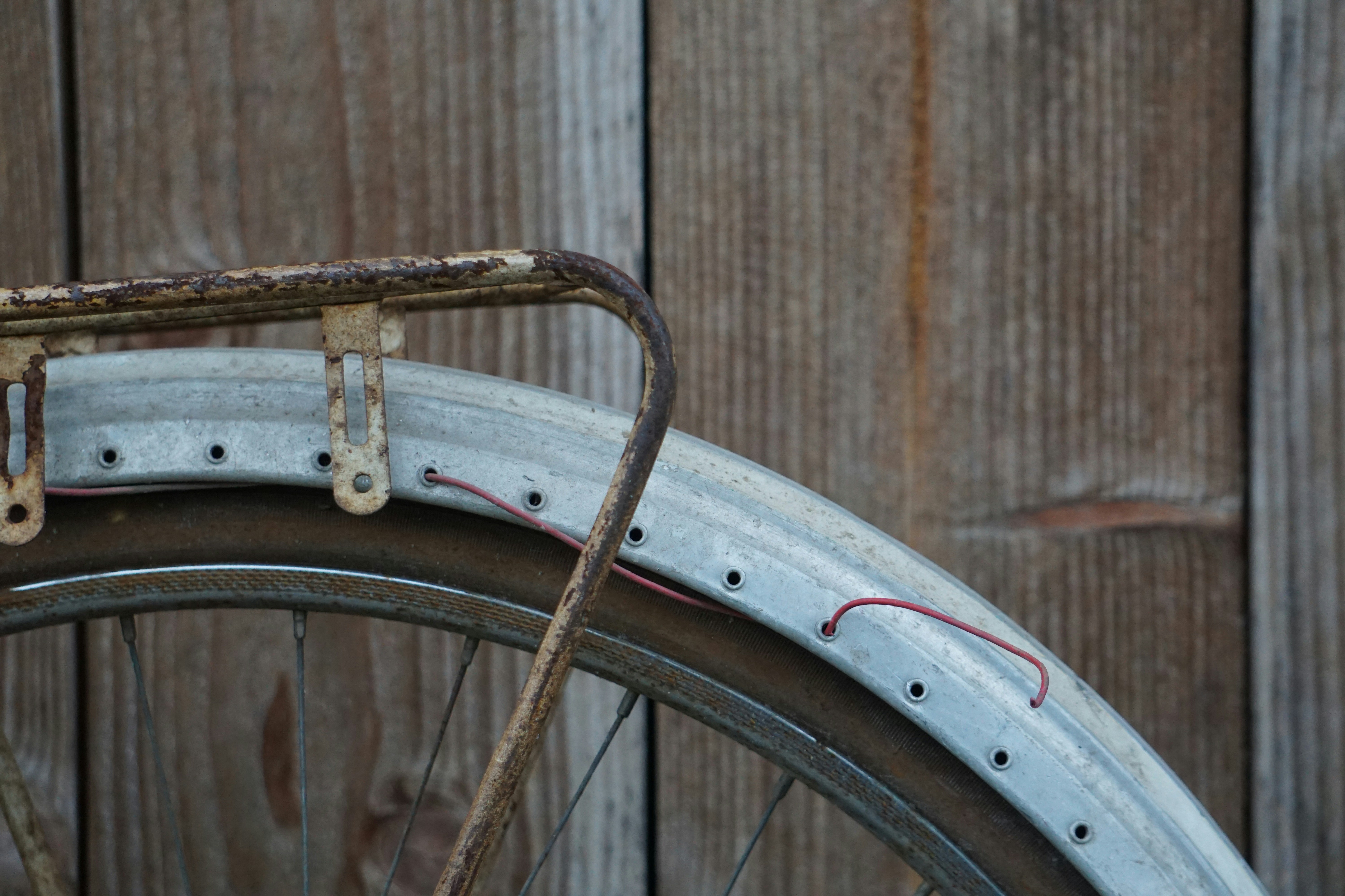 Close-up of a weathered bicycle wheel resting against a rustic wooden backdrop, highlighting the intricate details of rust and wear.