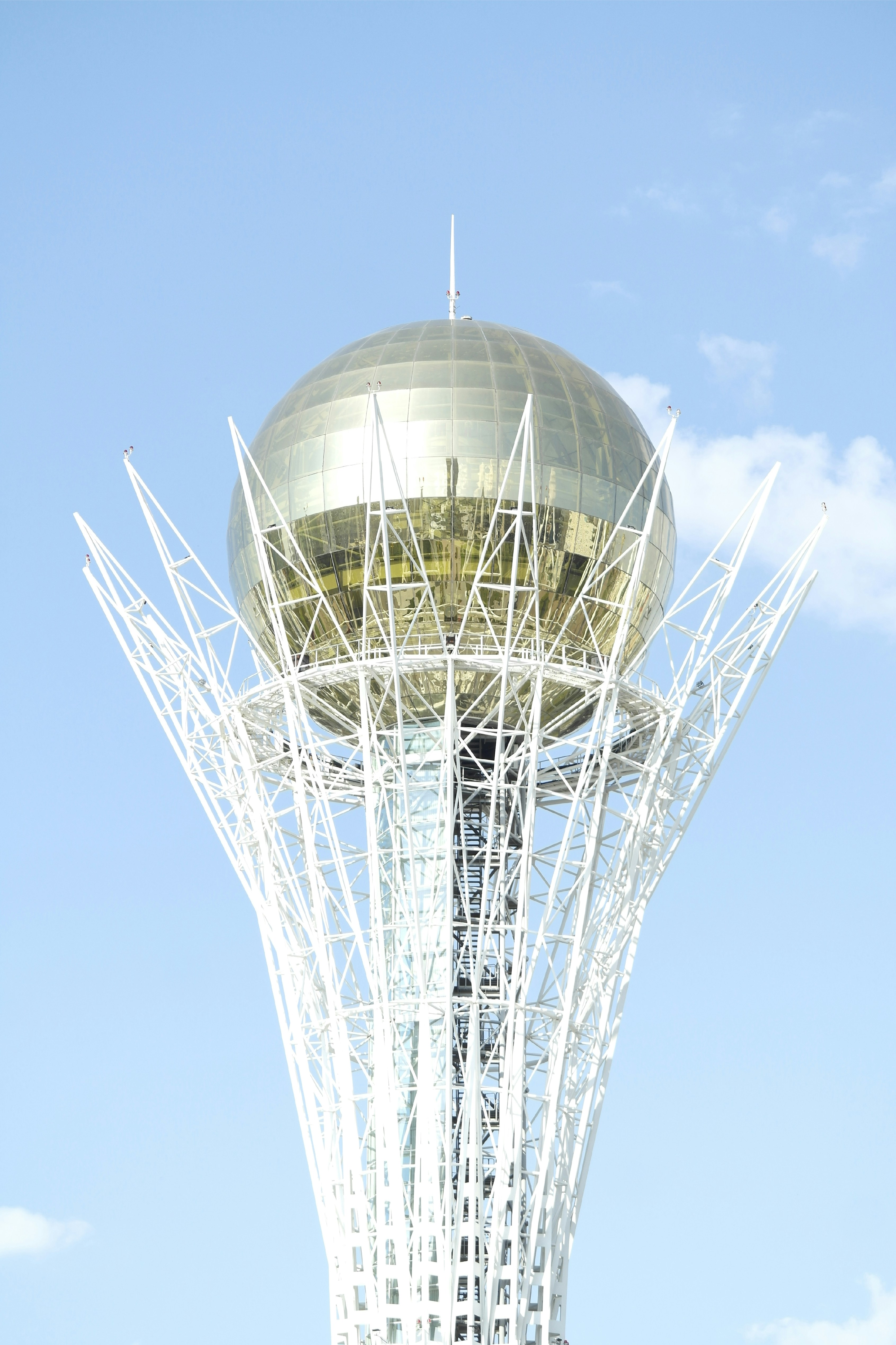 A striking tower with a reflective golden sphere atop a delicate white framework, set against a clear blue sky.