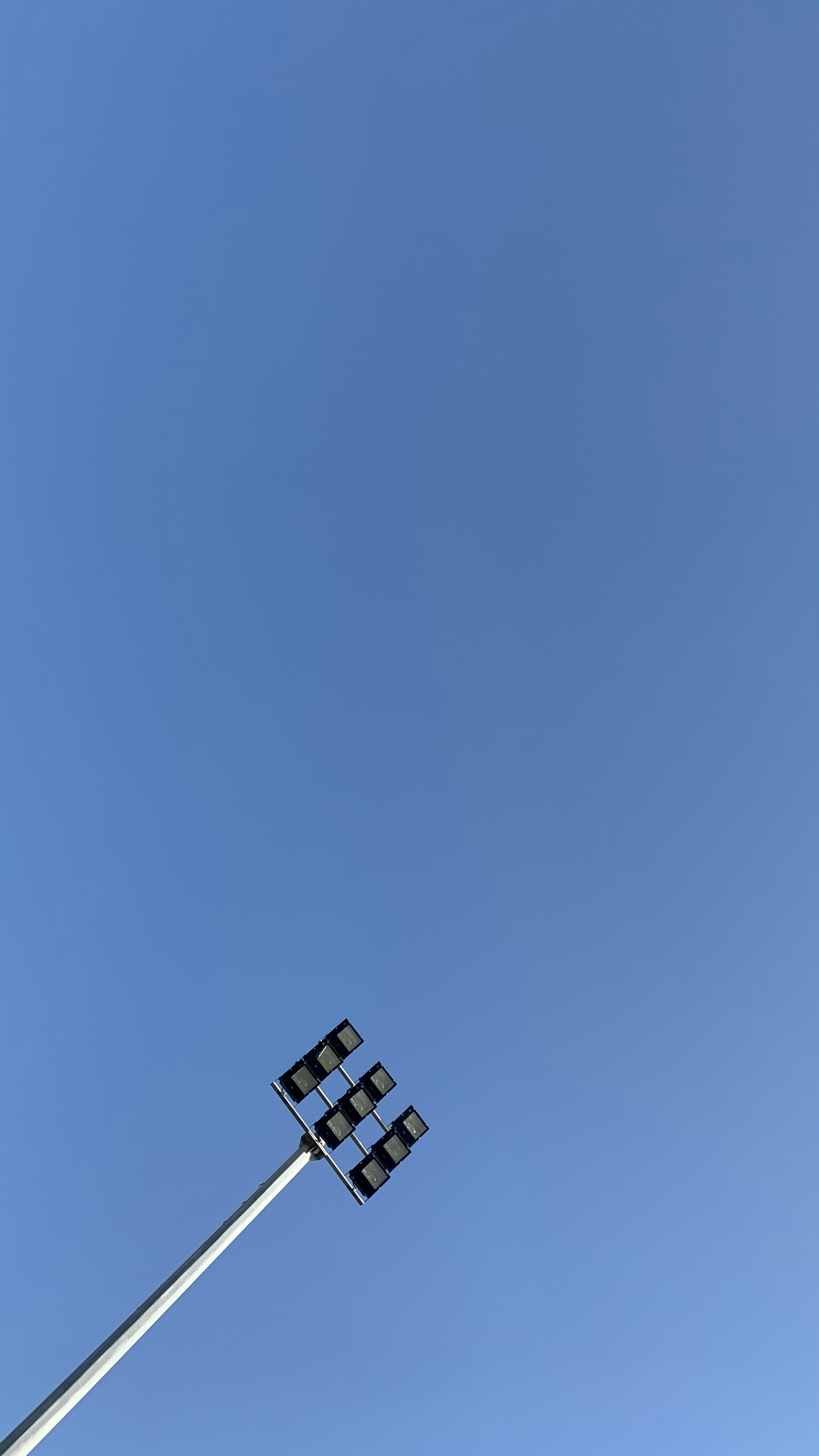 Floodlight tower reaching into a clear blue sky, showcasing a minimalist composition.