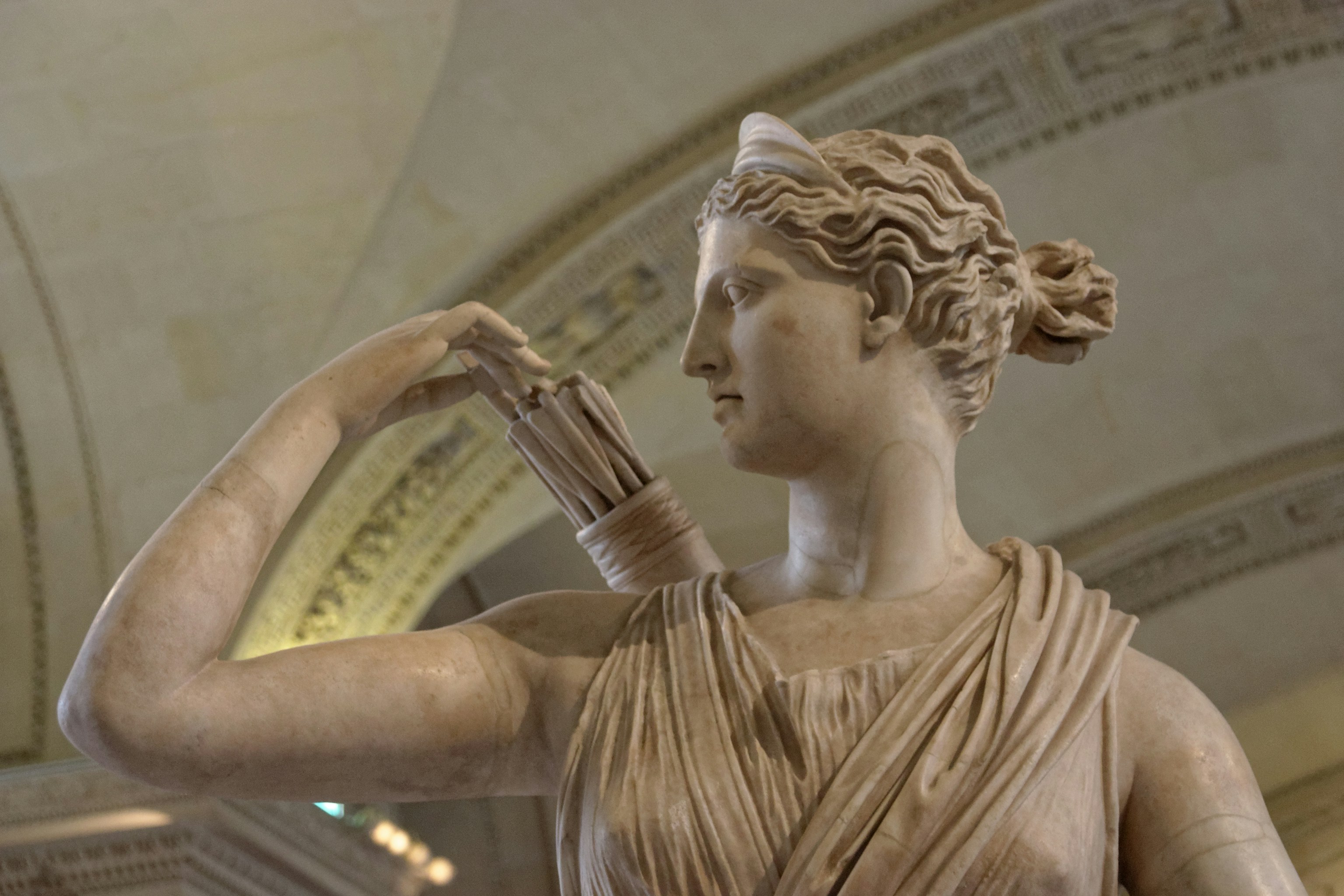 Classical sculpture of a female figure holding an arrow, symbolizing strength and focus in a museum setting.