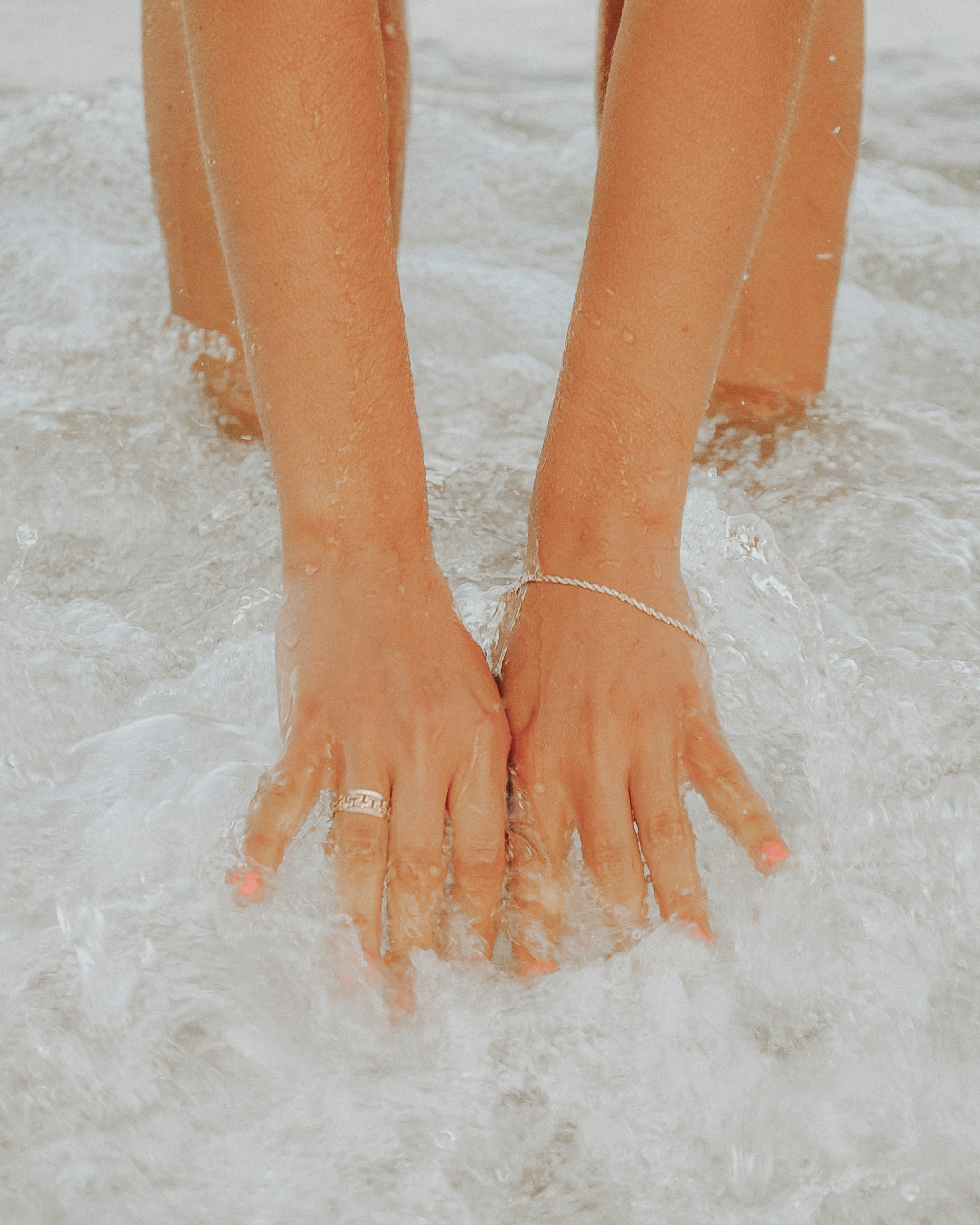 Hands submerged in gentle ocean waves, adorned with delicate jewelry, capturing a moment of tranquility and connection with nature.