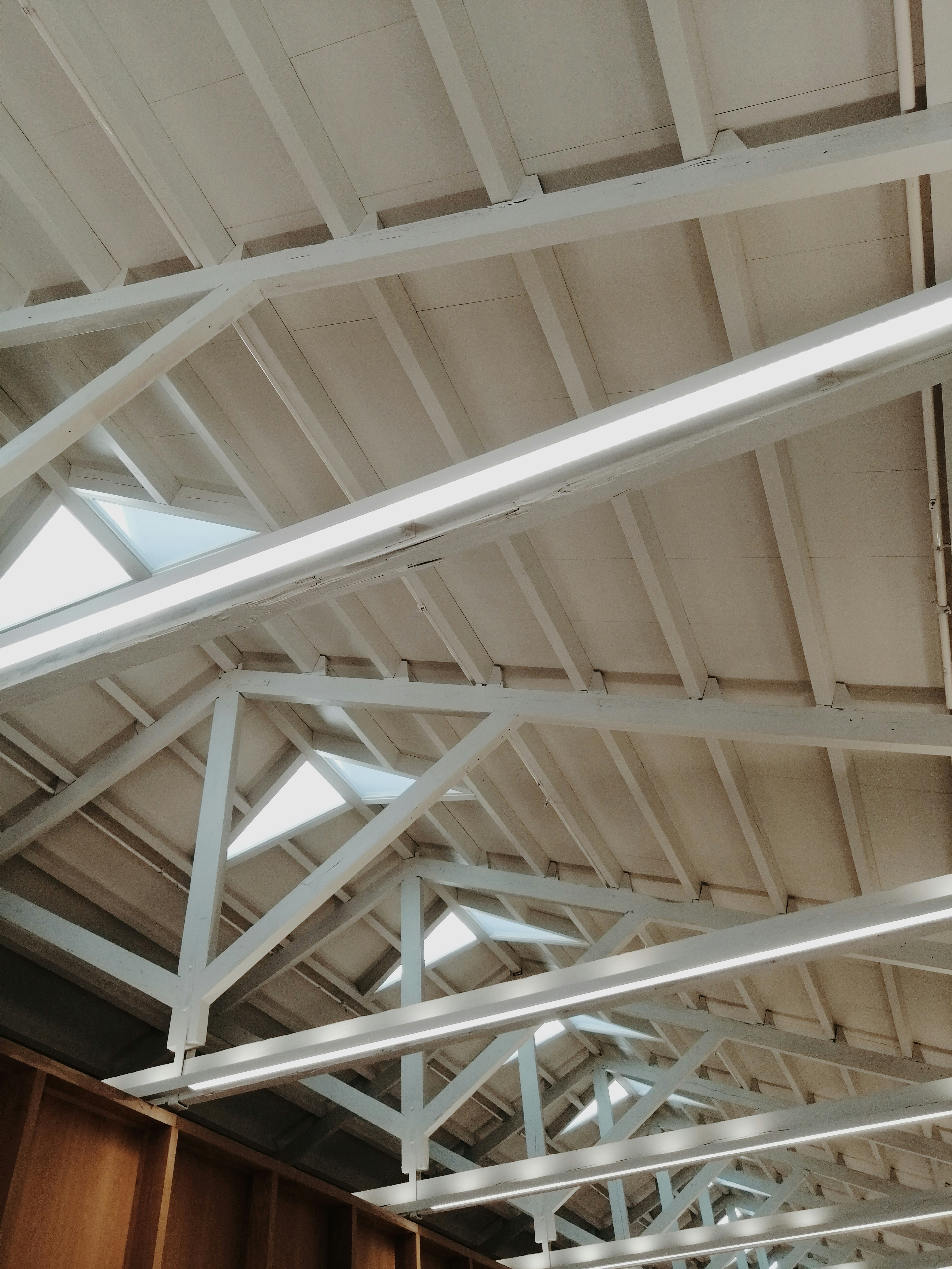 Intricate wooden beams and skylights converge in a modern architectural space, showcasing a blend of natural light and design elements.