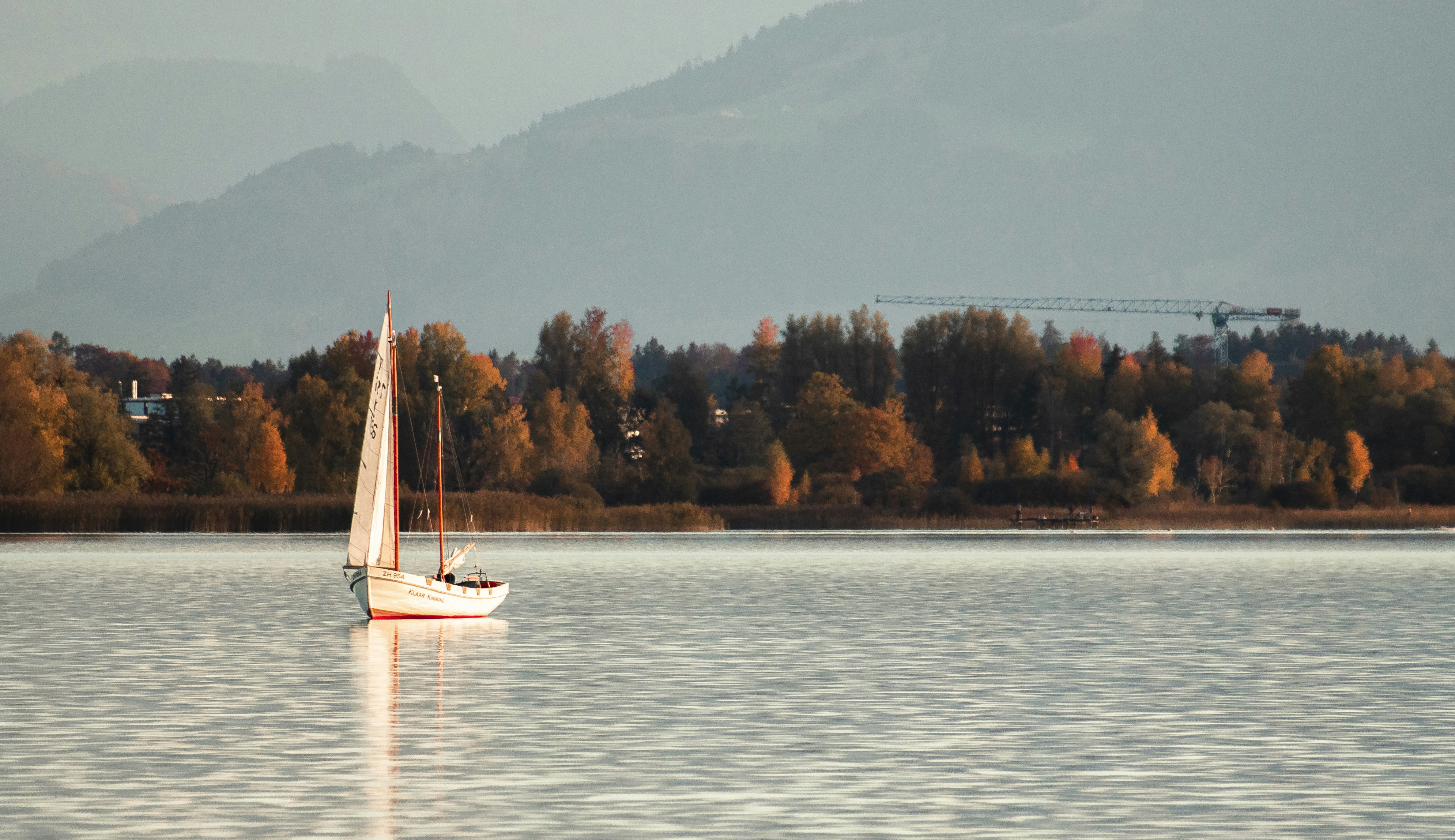 Autumn Sail: A Lone Craft on a Glassy Lake Beneath Distant Peaks