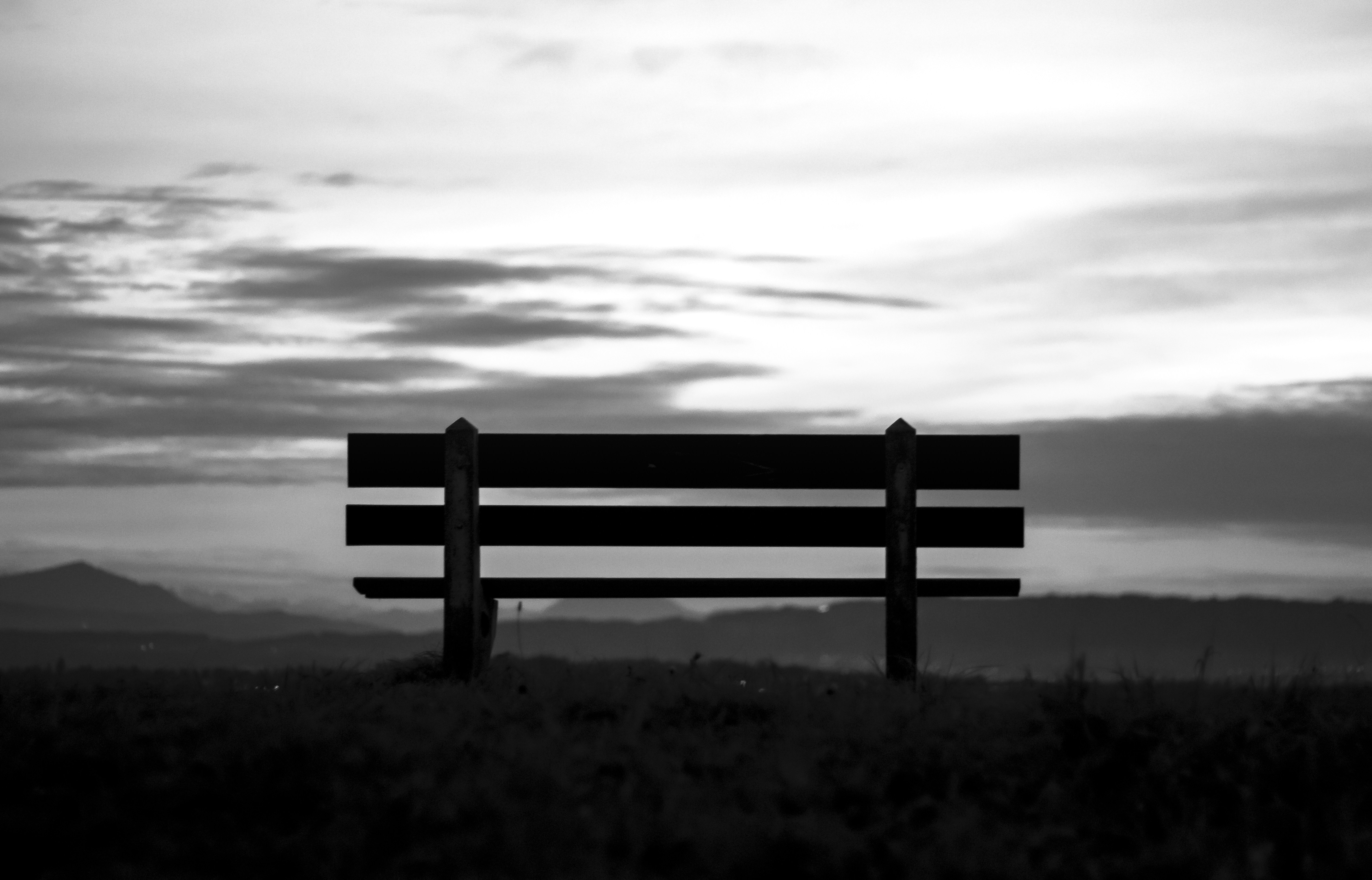 Lonely wooden bench silhouetted against a moody twilight sky, inviting contemplation. The scene captures the essence of solitude in nature.