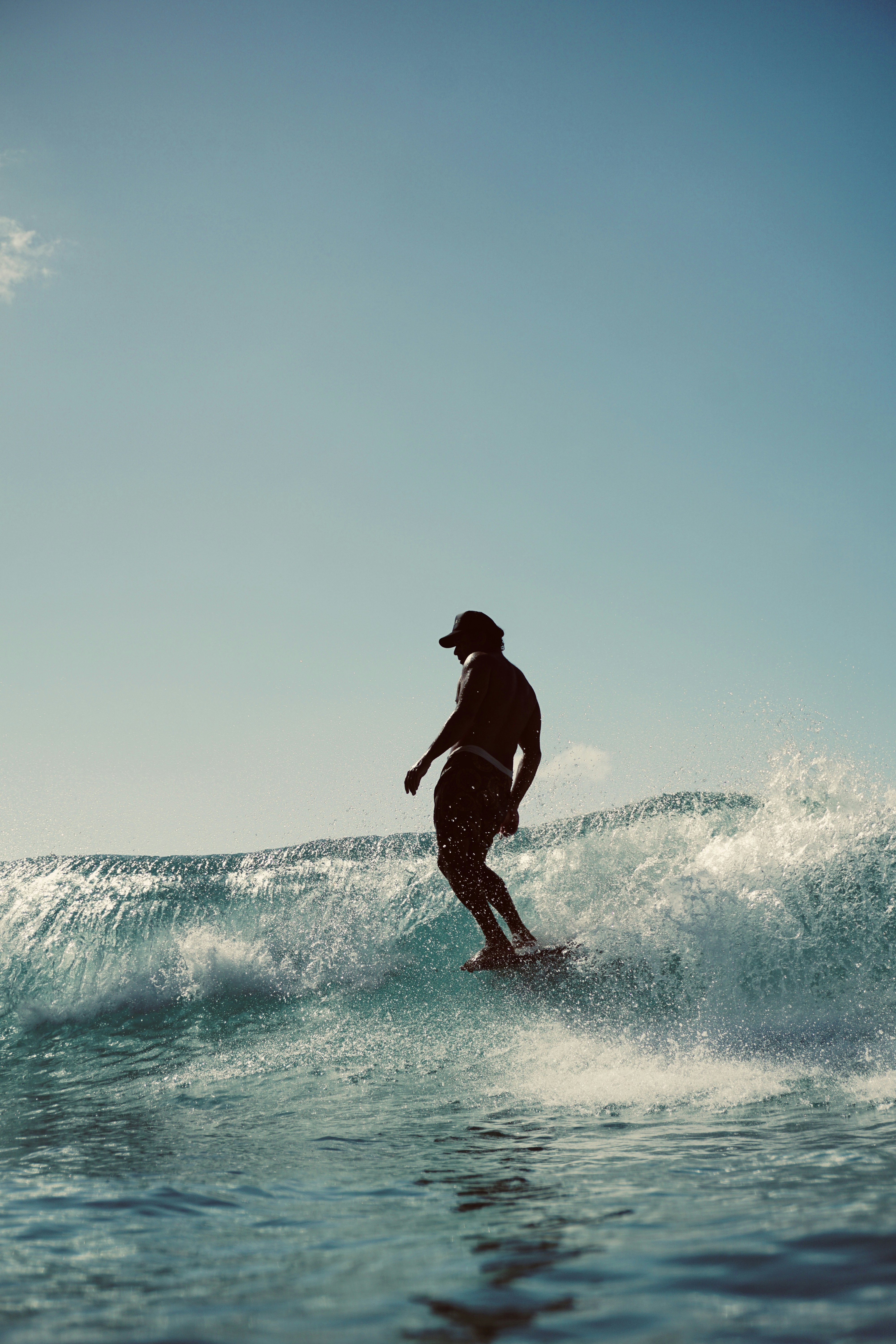 Silhouette of a surfer gliding gracefully atop a wave under a clear blue sky.