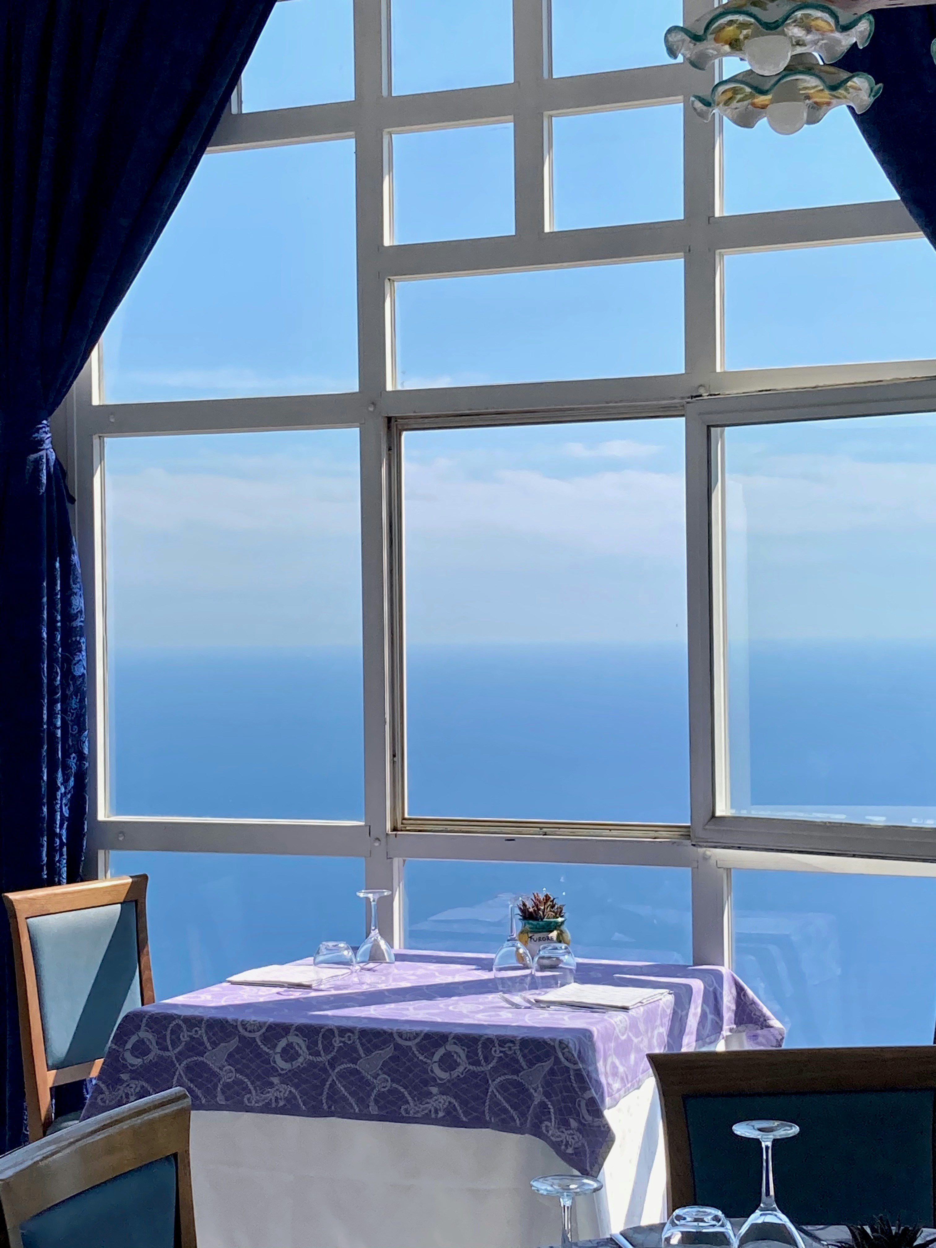 Elegant dining setup with a purple tablecloth and ocean view framed by large windows and blue curtains.