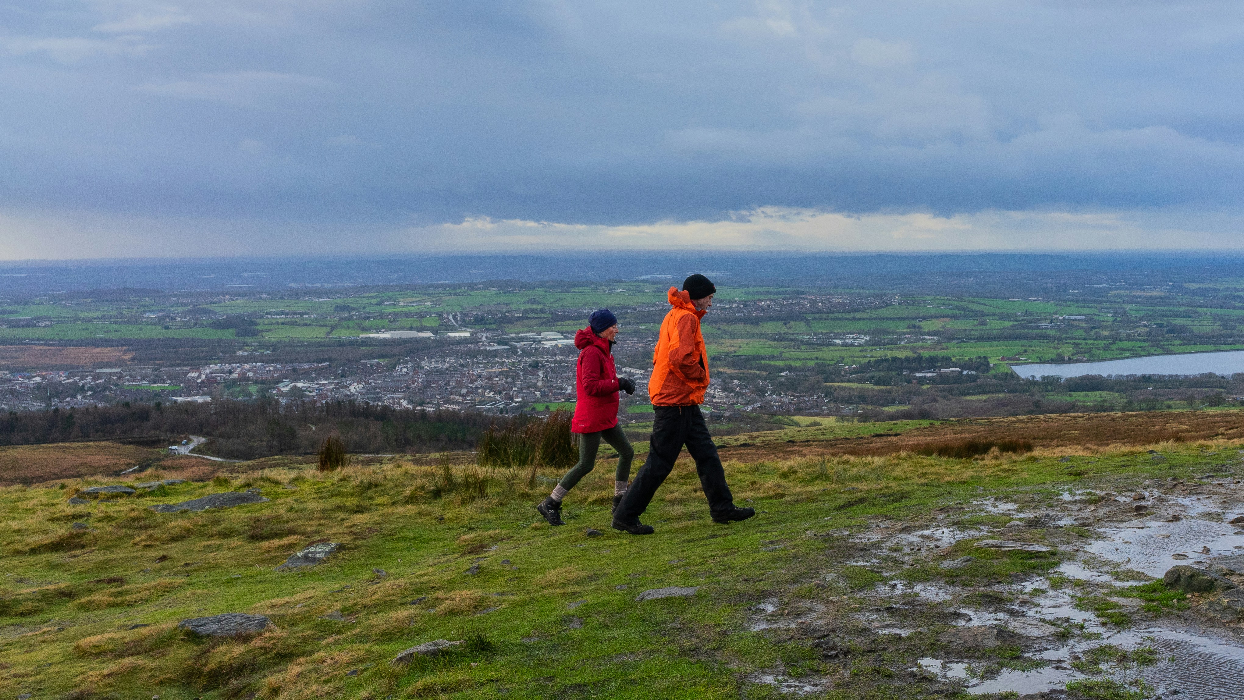 Ridge Walkers in Bright Jackets Crossing a Wind-Swept Moor Over a Patchwork Valley
