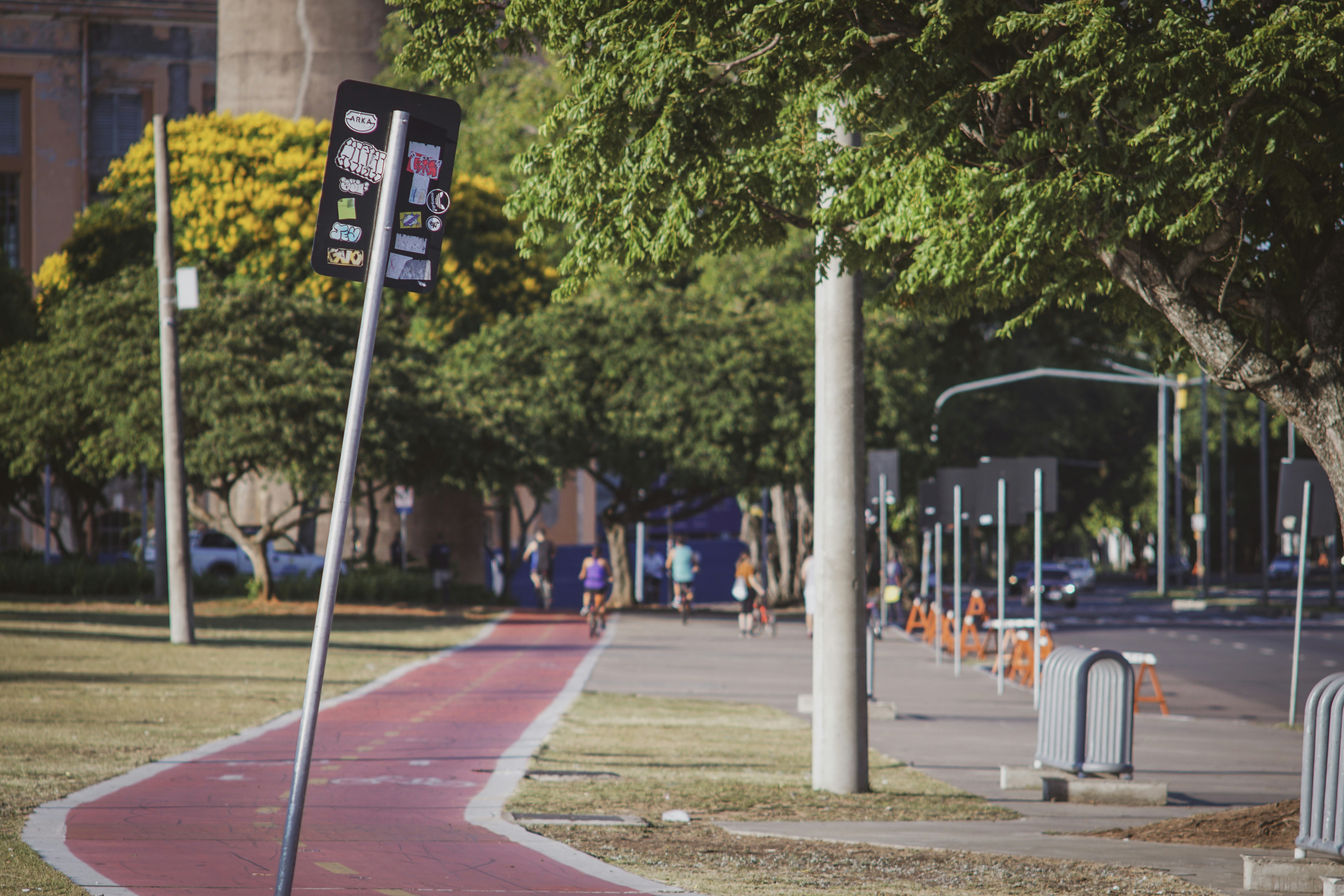Leaning street sign along a red bike path bordered by lush, green trees.