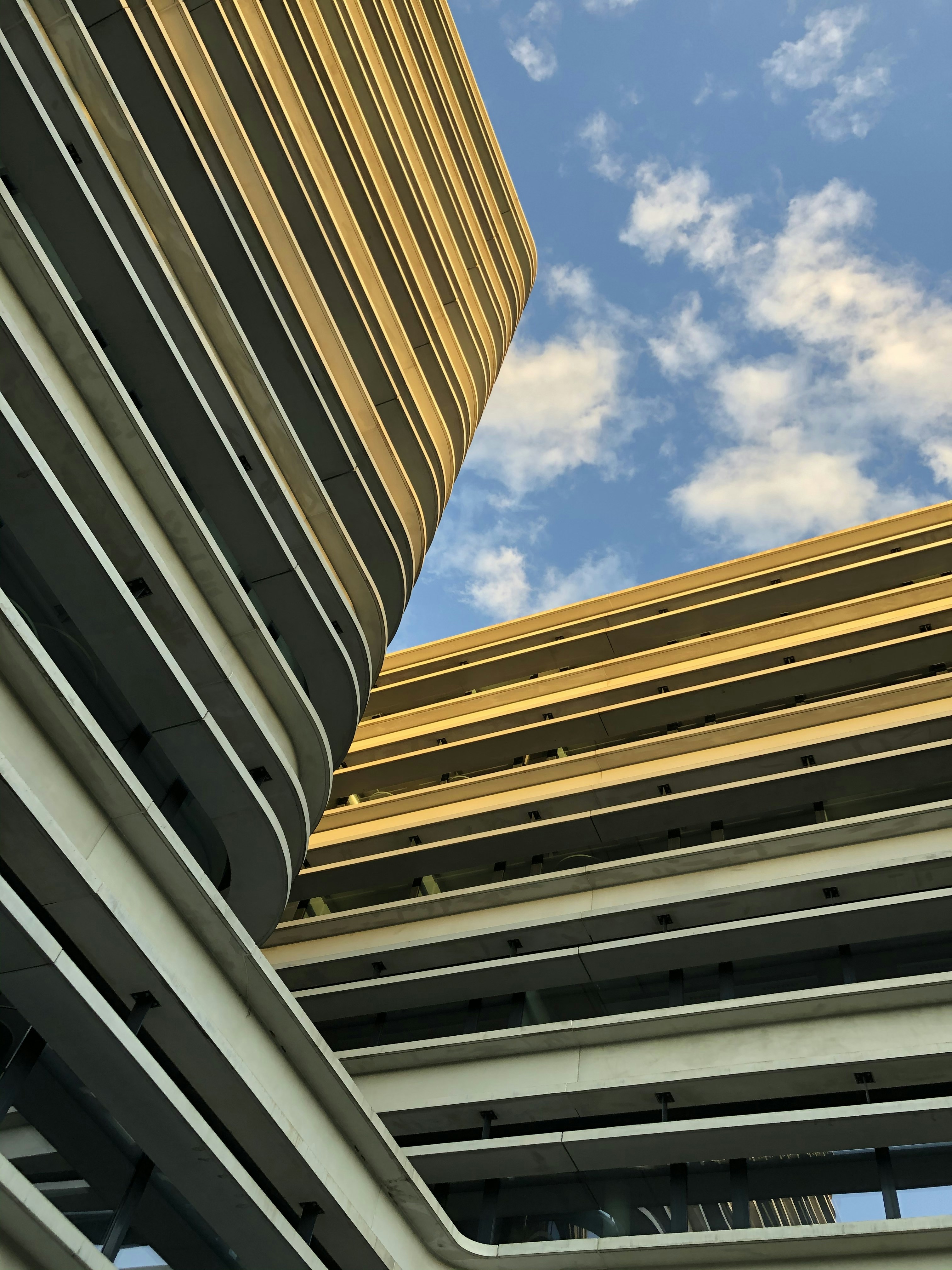 Abstract view of modern architecture featuring layered, curving lines against a blue sky with scattered clouds.