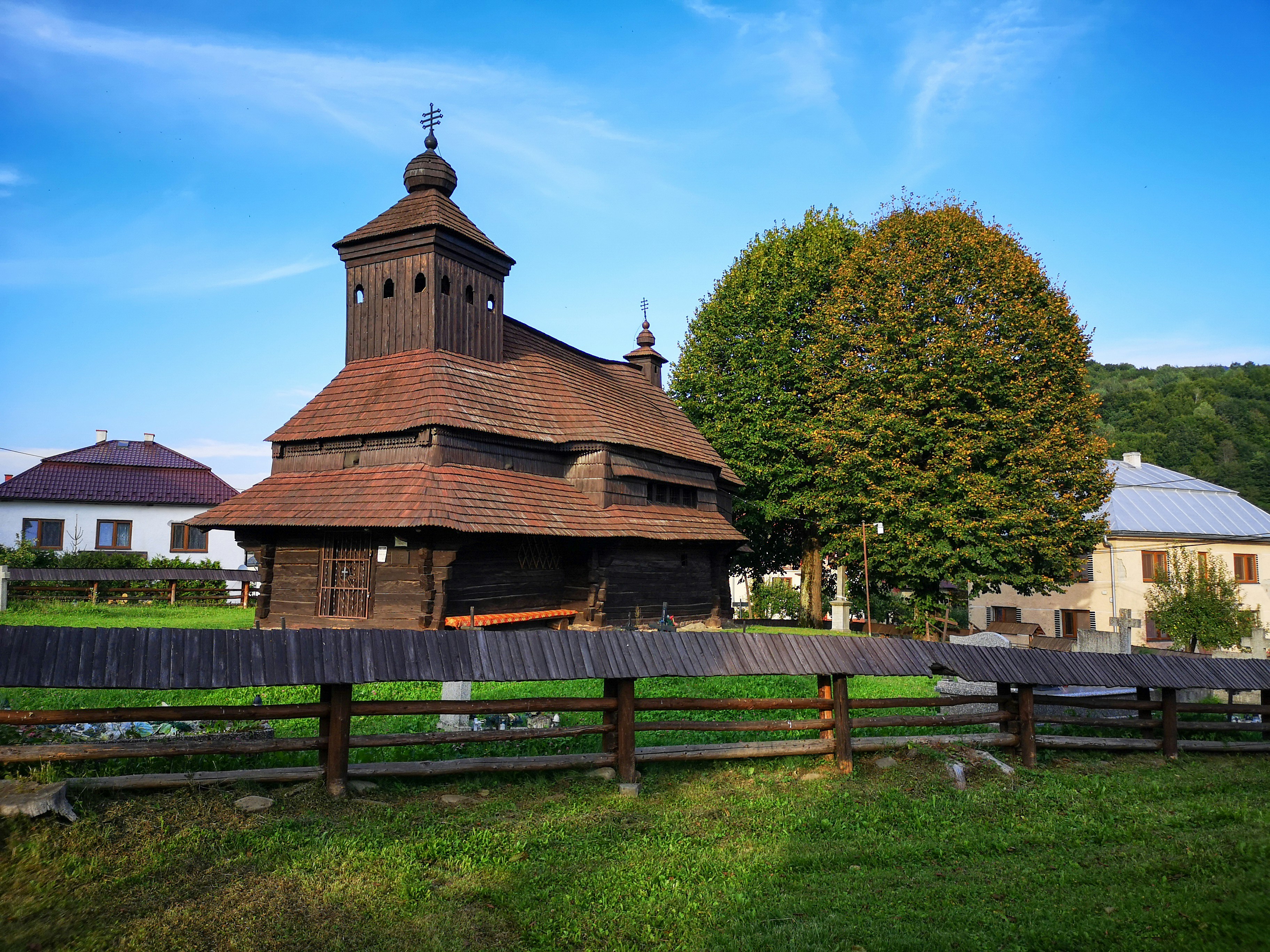 Historic wooden church with intricate architecture surrounded by lush green trees under a clear blue sky.