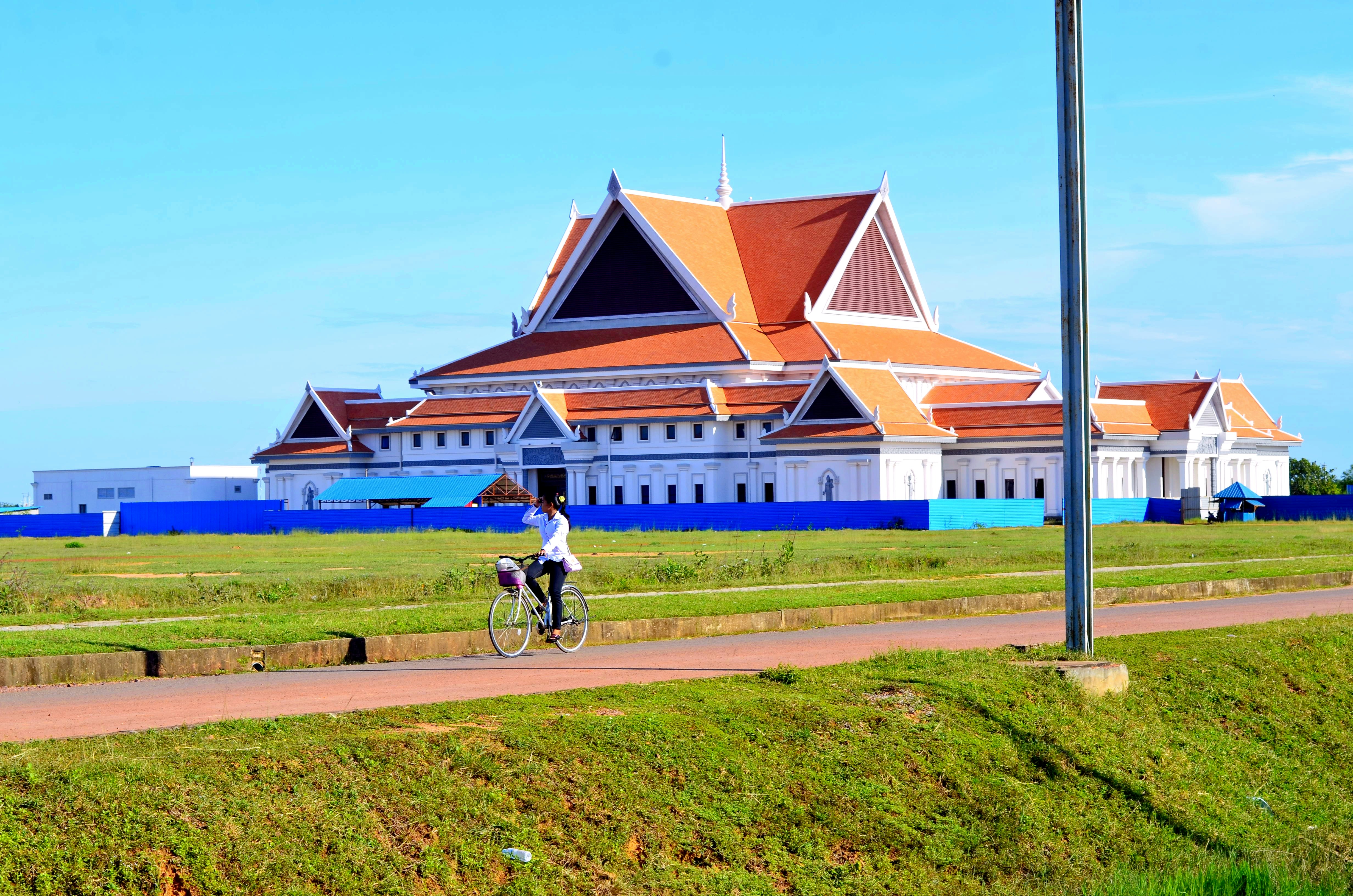 Cyclist on a sunlit park path before a coral-roofed temple