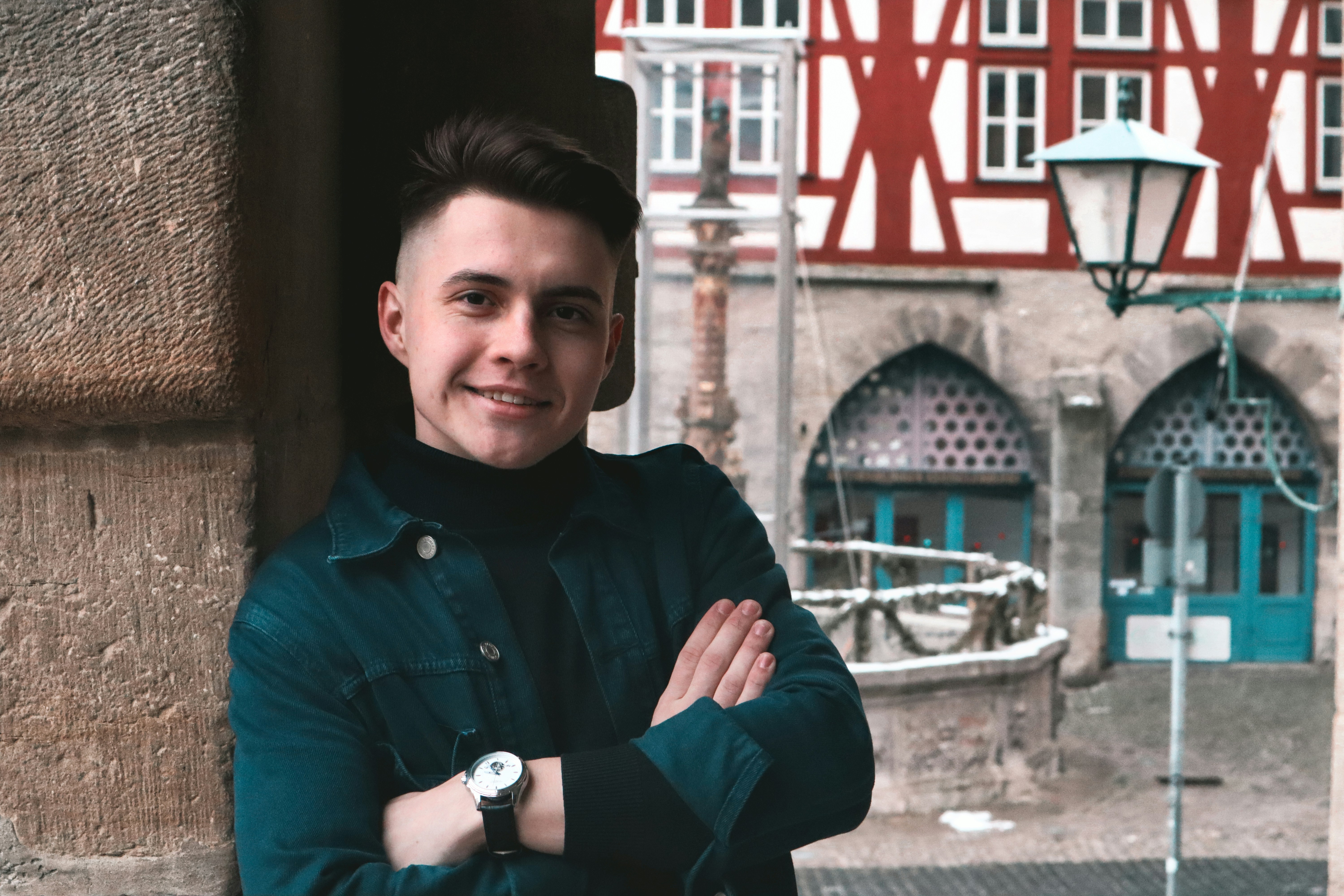Young man posing confidently against a historic backdrop with architectural details and a lantern. The scene reflects a blend of modern style and classic architecture.