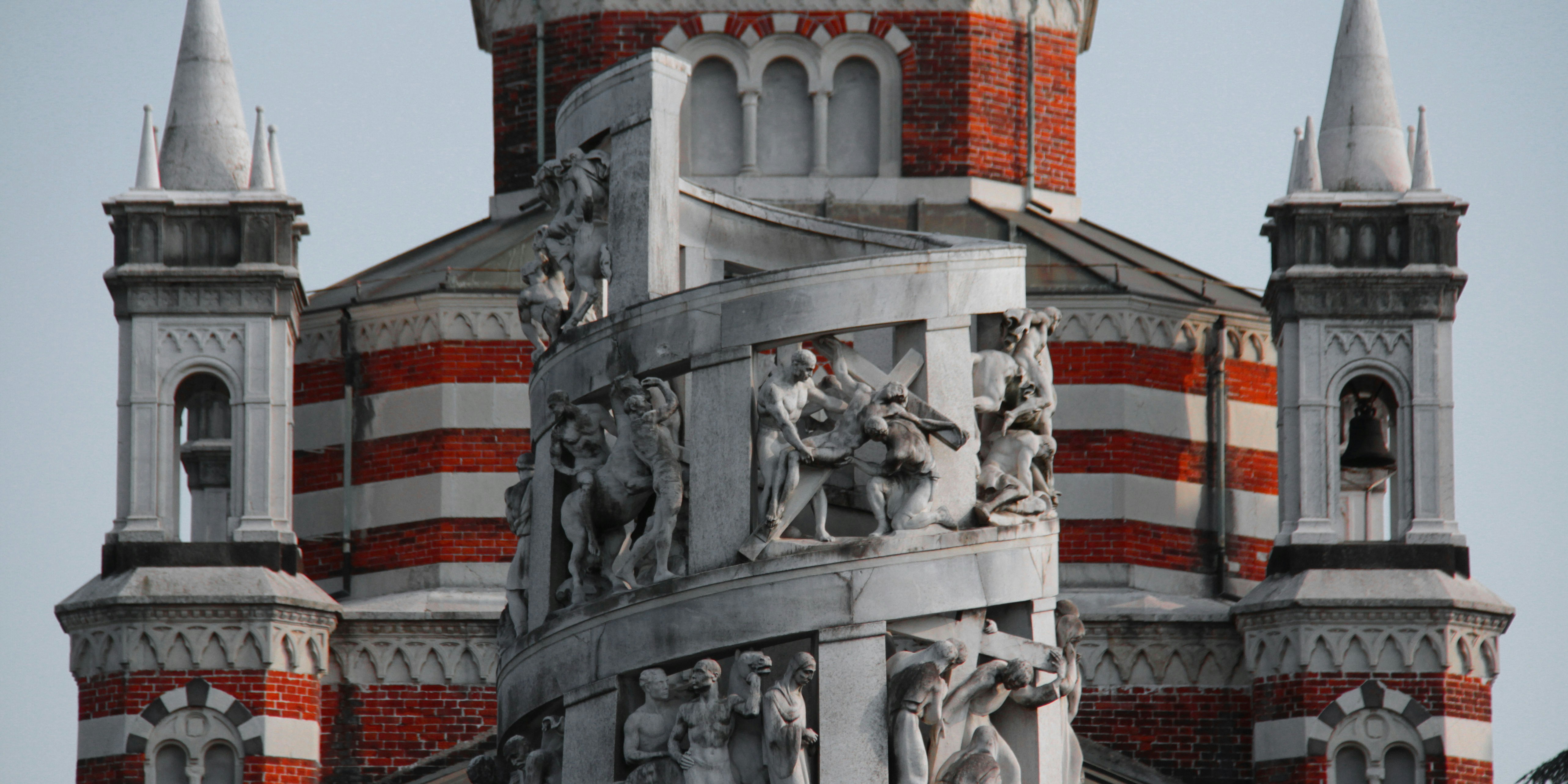 Intricate stone sculptures adorn a spiraling column atop a striking red-brick building, highlighting the artistry of historical architecture.