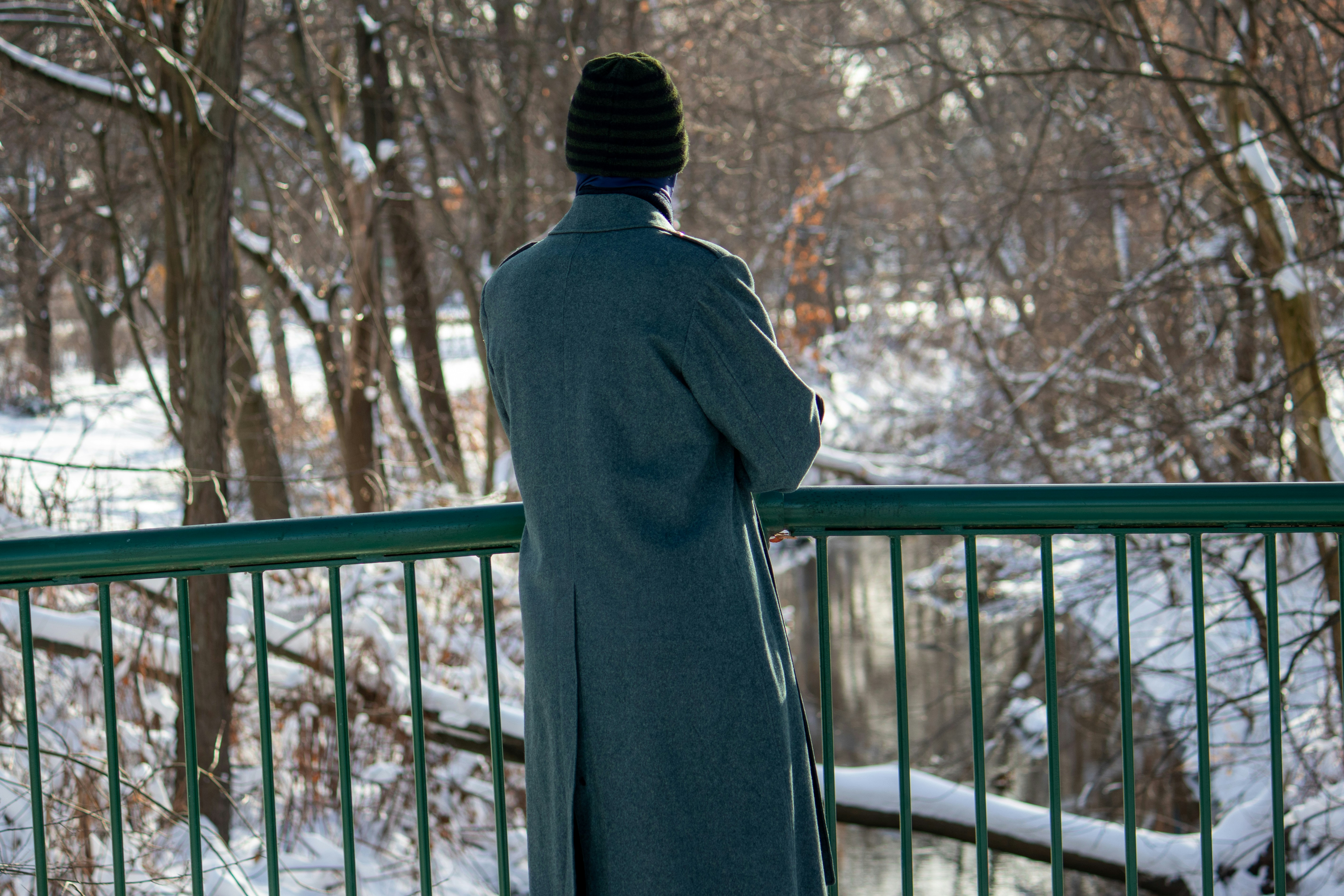 man in gray coat standing near brown wooden fence during daytime
