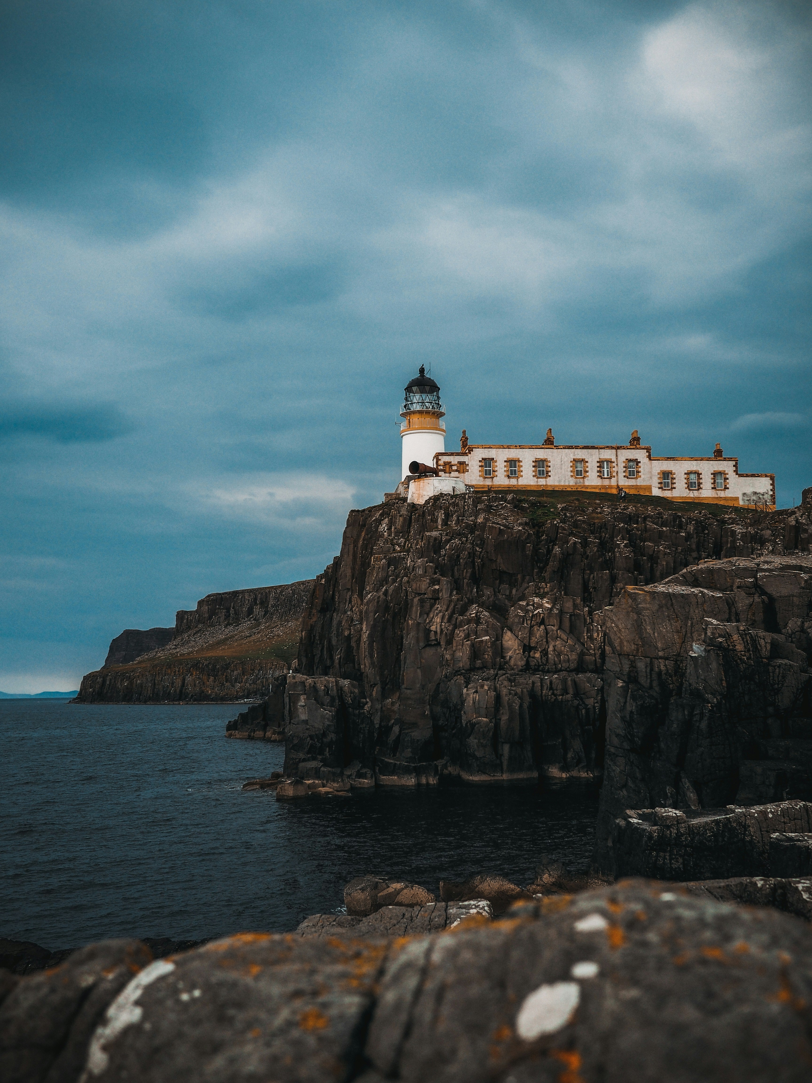 A lighthouse perched on a rocky cliff, overlooking the turbulent sea under a moody sky.
