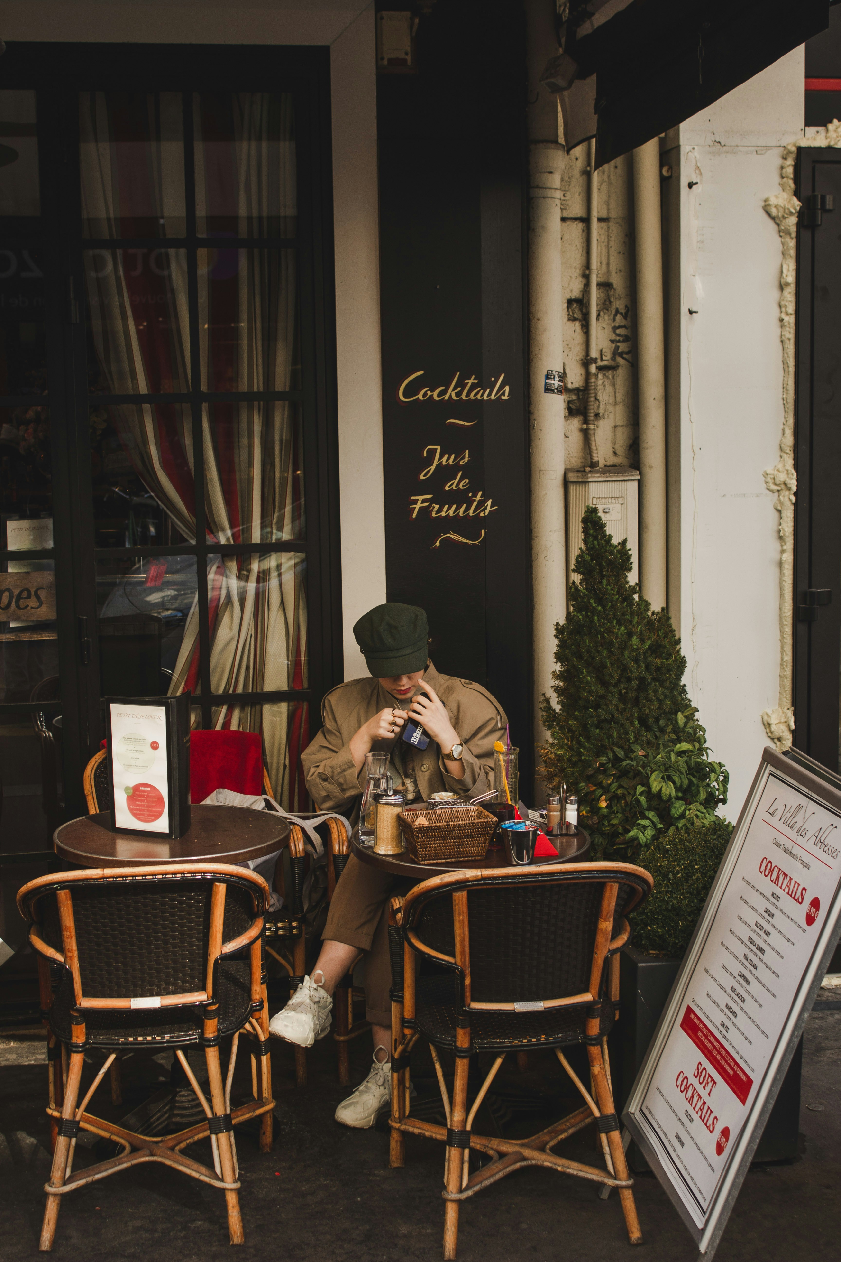 Café Side Moment: A lone patron in a green cap sips beneath striped curtains