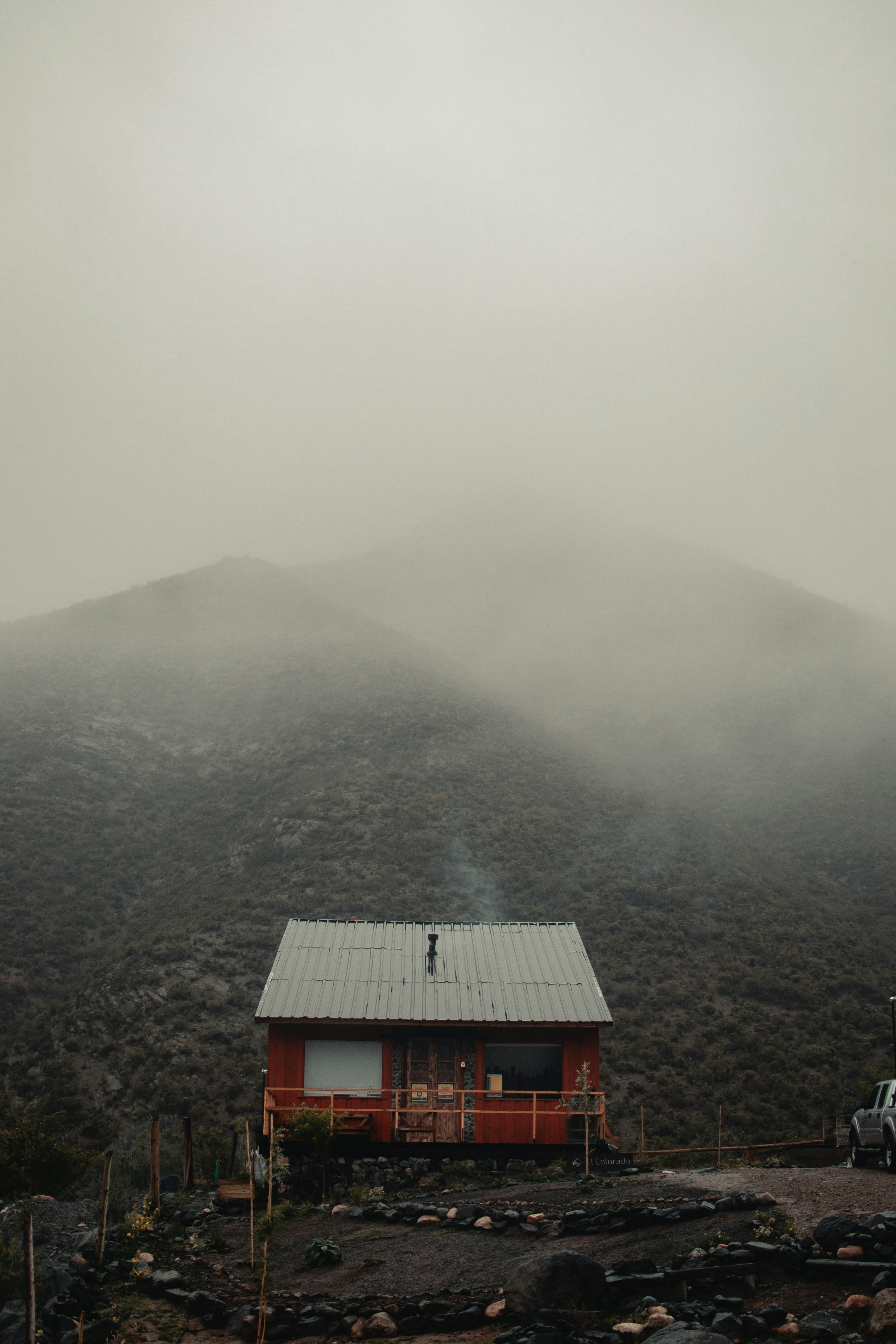 A solitary red cabin nestled against a foggy mountain backdrop, exuding a sense of tranquility and isolation.