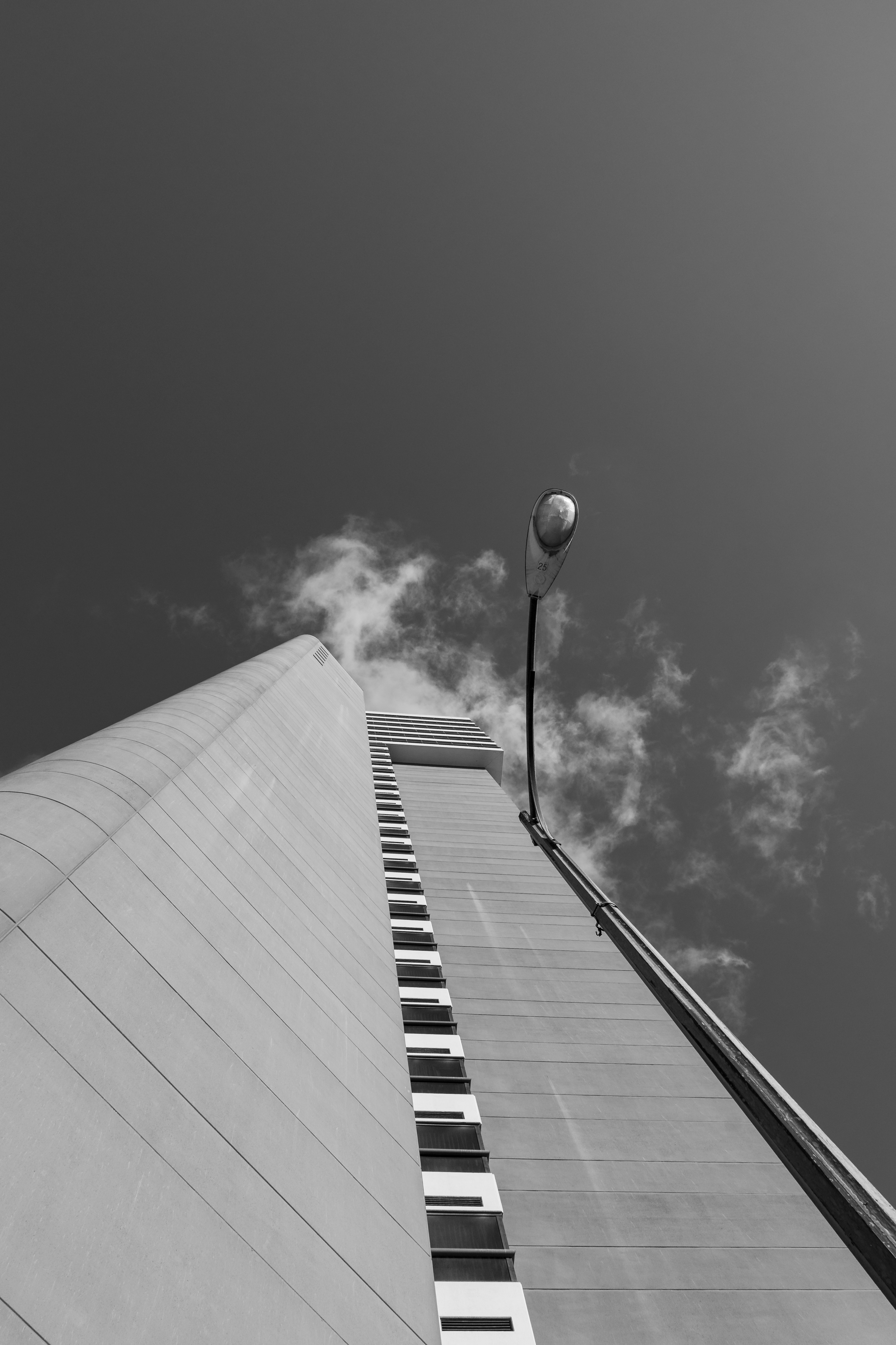 Monochrome photograph showcasing a towering building with a streetlight in the foreground and wispy clouds above.