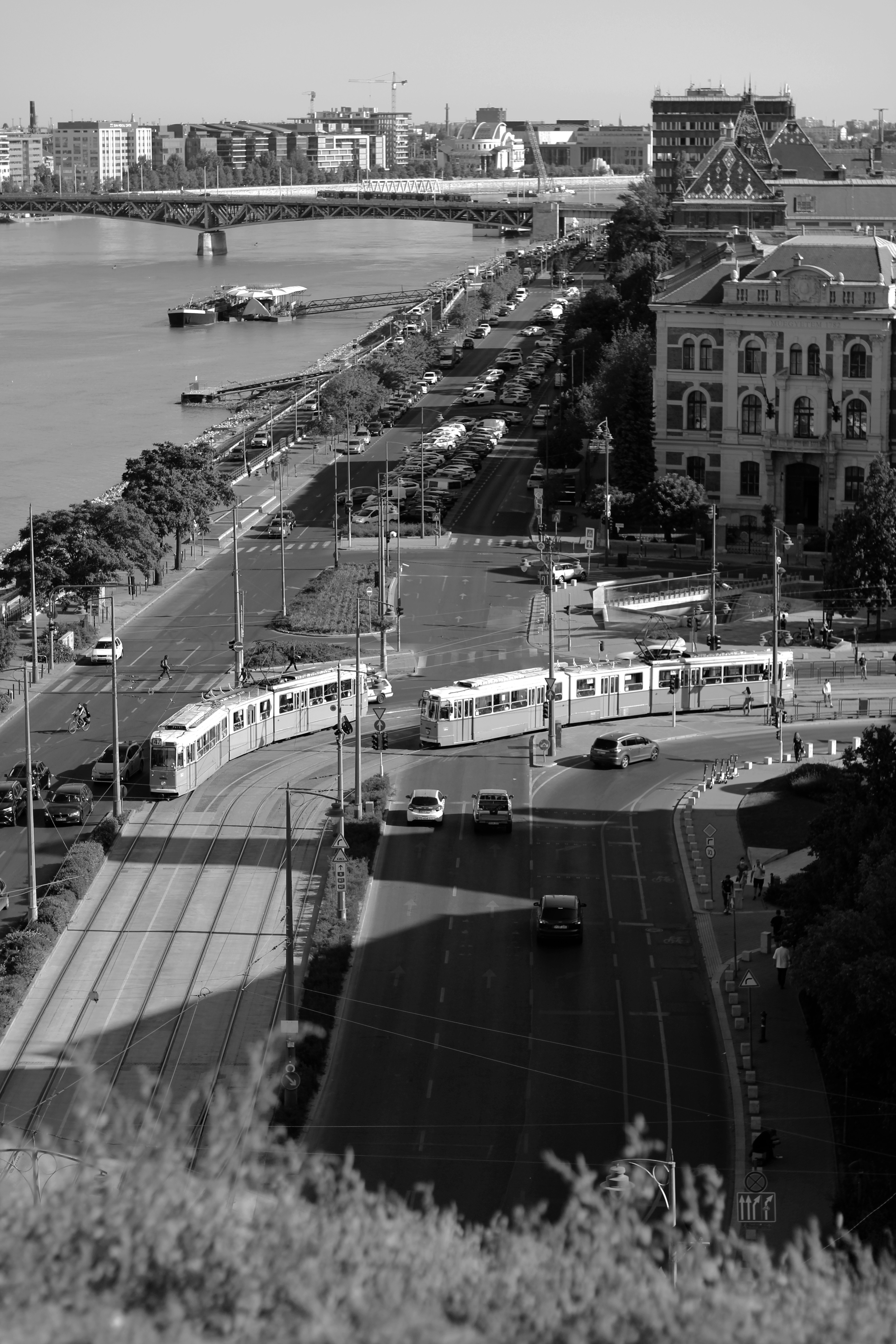 A busy intersection featuring a tram navigating a curved track alongside flowing traffic and pedestrians, set against a riverside backdrop.