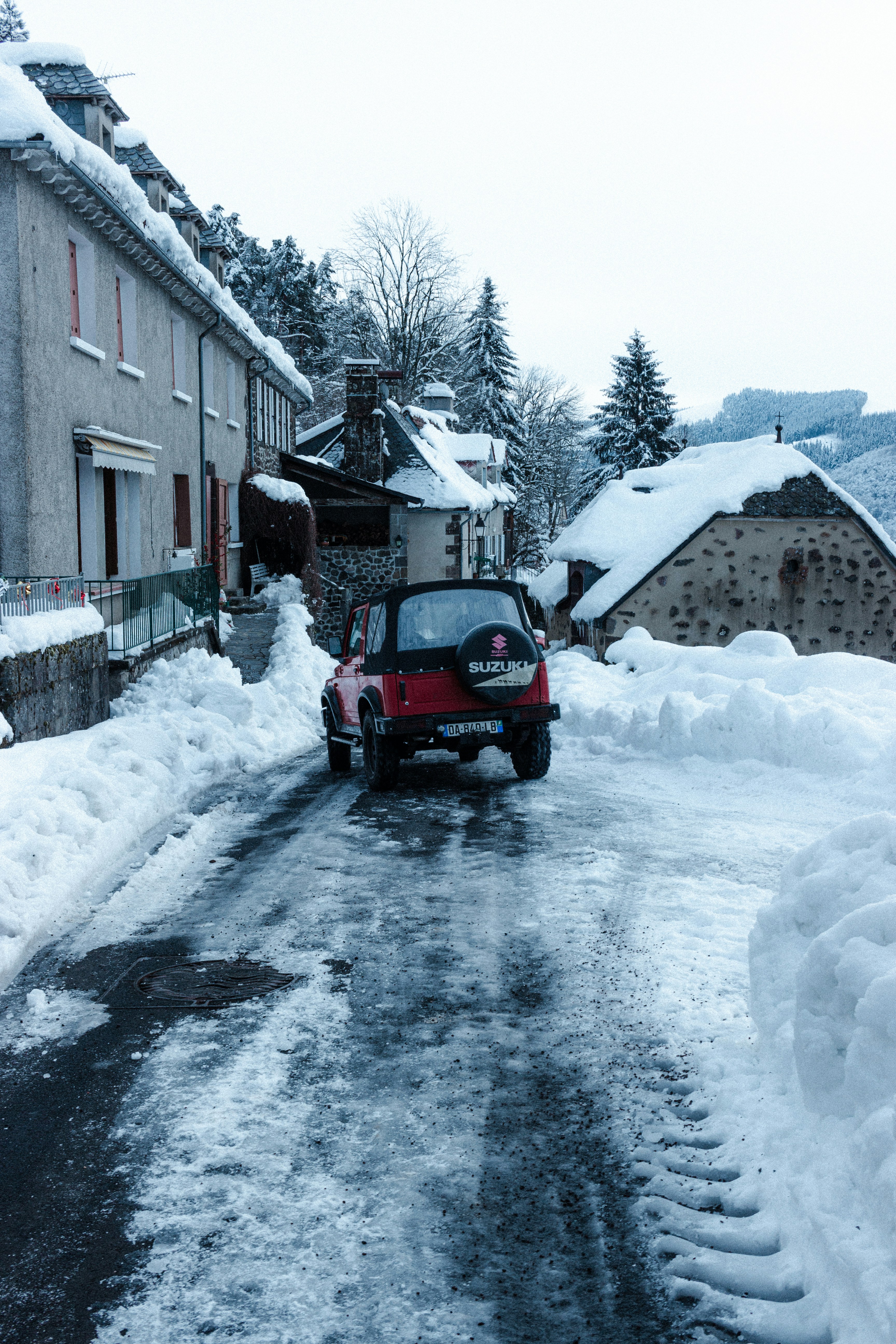 Snow-Capped Village Lane: Red Suzuki on a Slushy Street