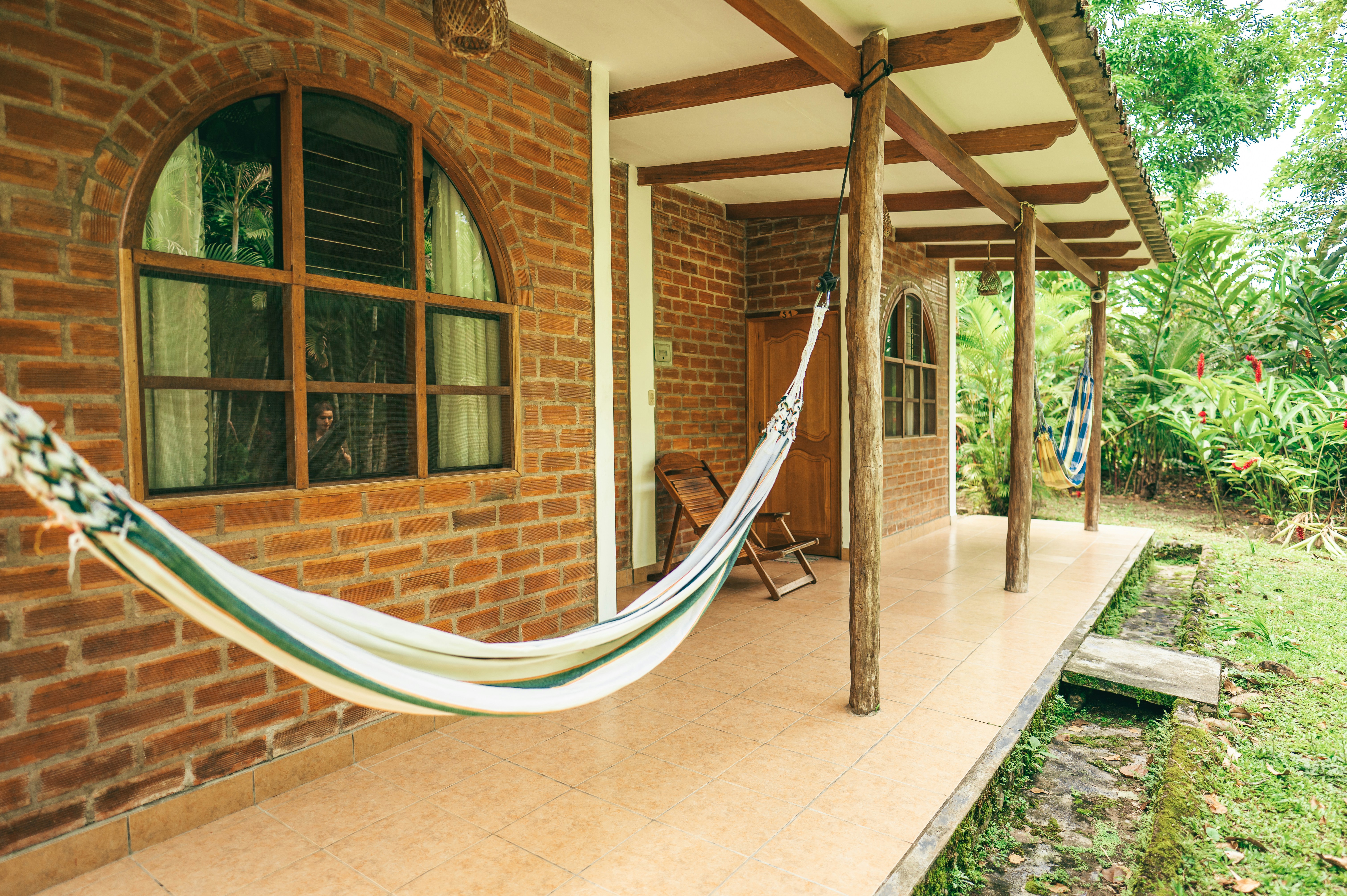 Hammock suspended on a rustic brick porch surrounded by lush greenery.