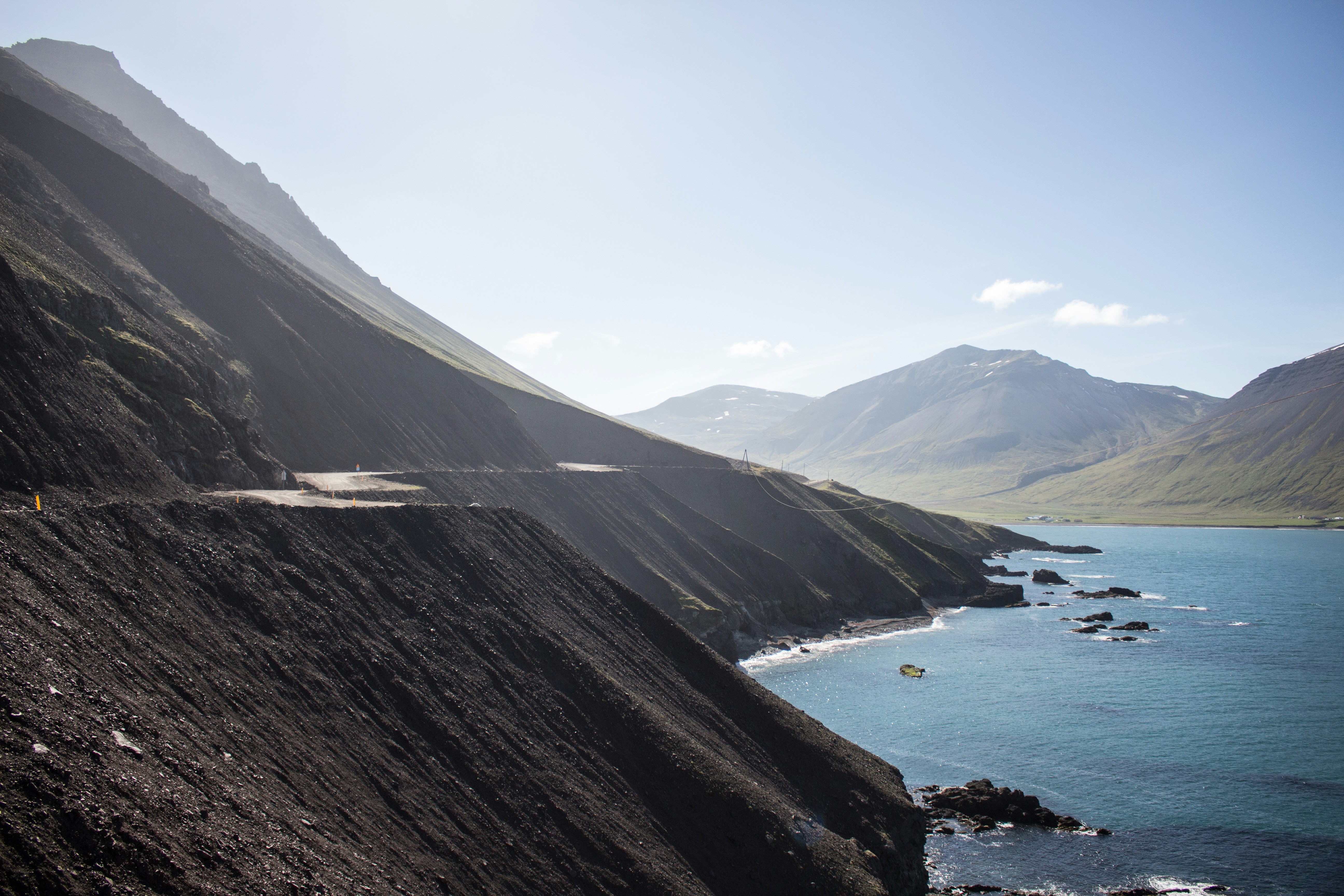 A winding road hugs the rugged coastline, flanked by steep mountains and tranquil blue waters. The scene captures the harmony between land and sea.