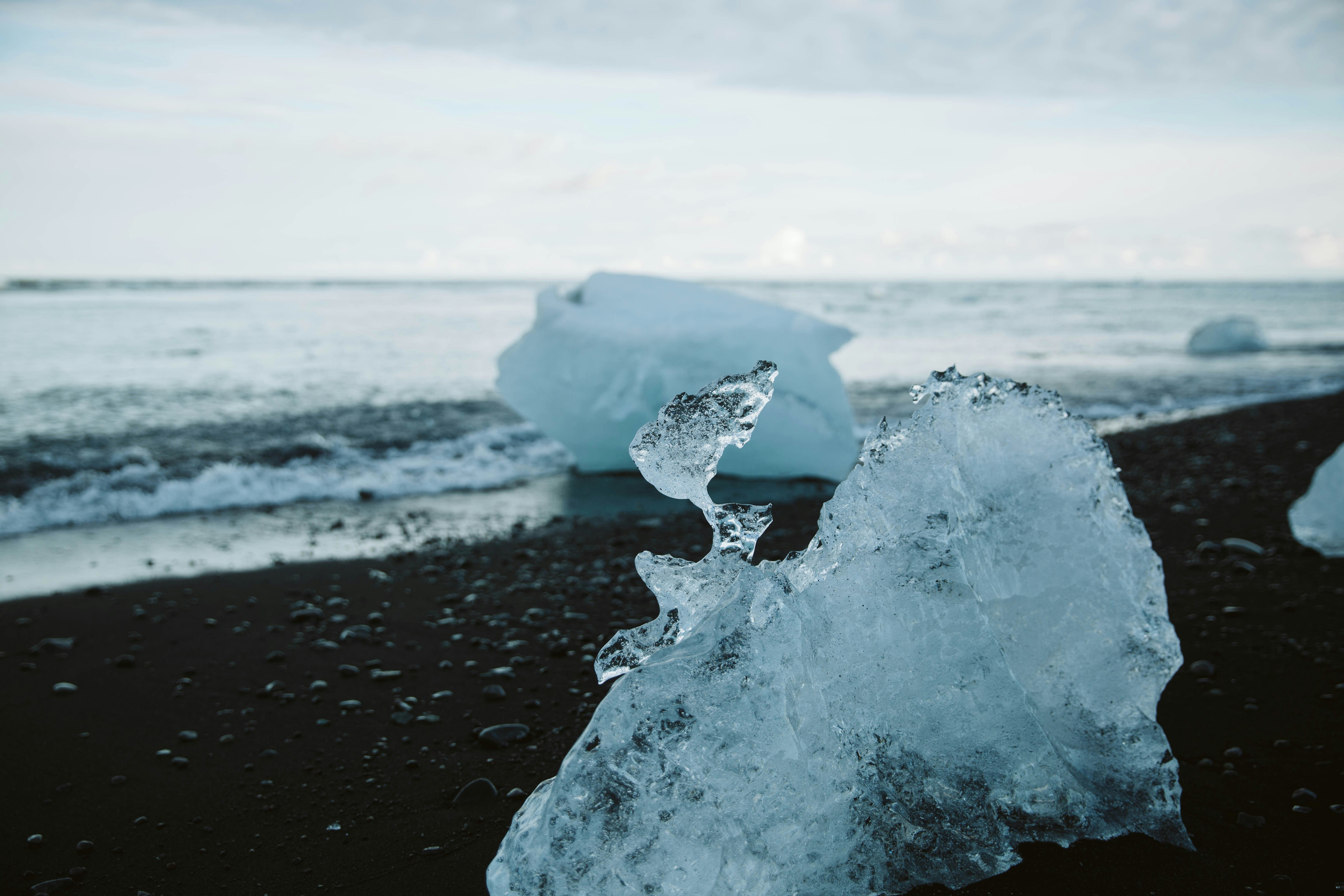 Intricate ice formations resting on a black sand beach, with gentle waves lapping at the shoreline. The serene atmosphere captures the interplay between land and sea.
