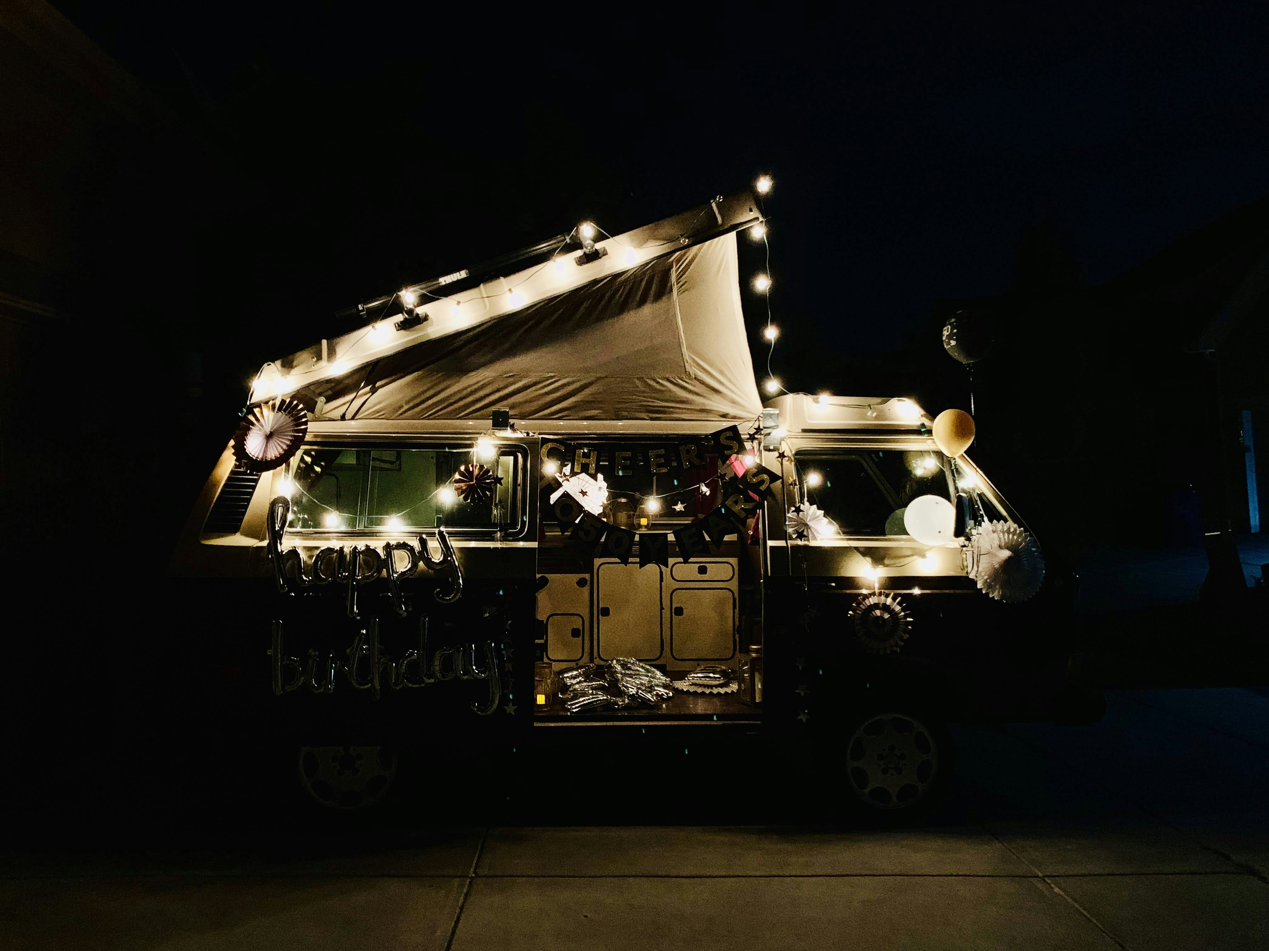 Vintage van adorned with birthday decorations and twinkling lights, creating a cheerful nighttime atmosphere.