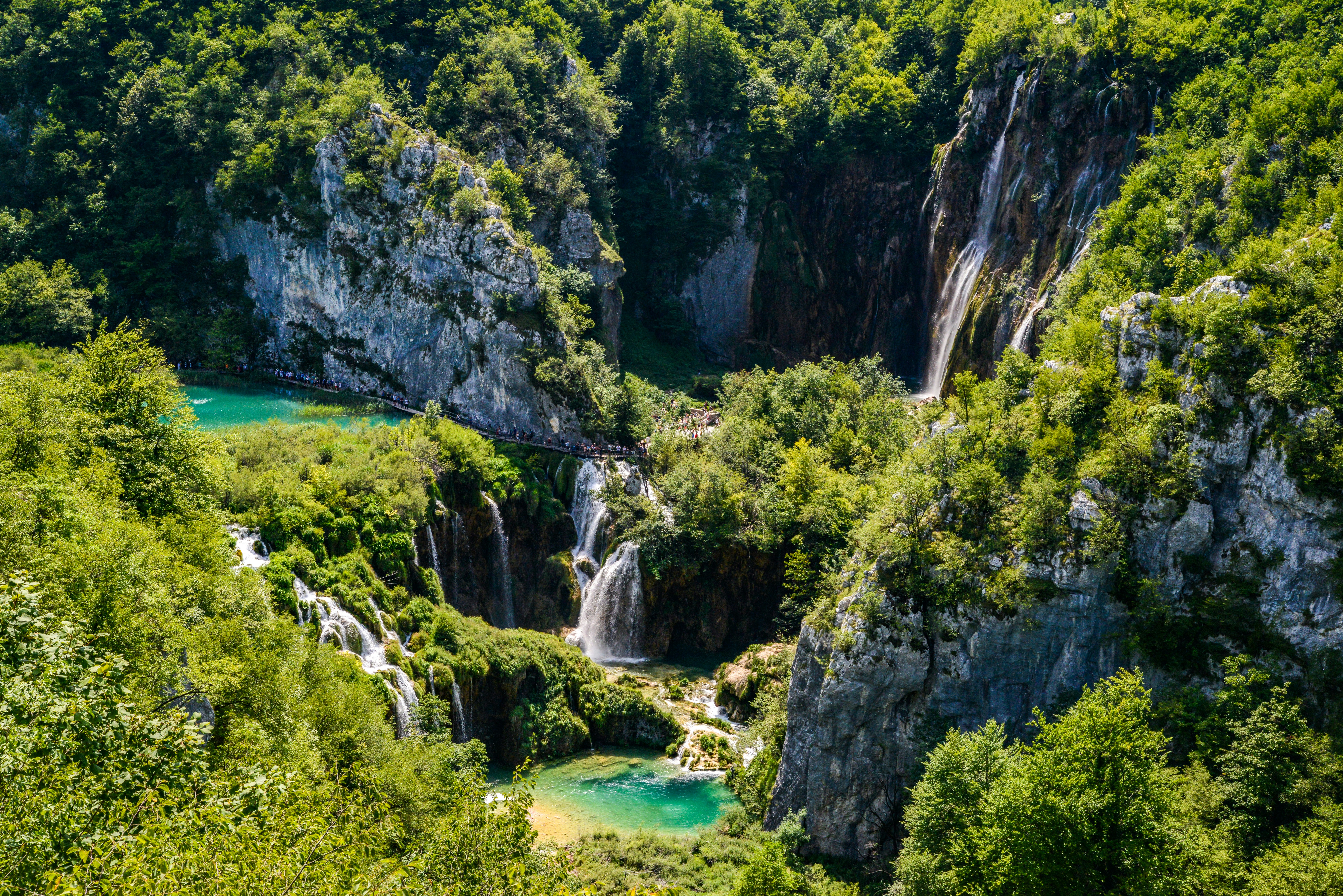 Aerial view of multiple waterfalls cascading into turquoise pools, surrounded by lush greenery and rocky cliffs.