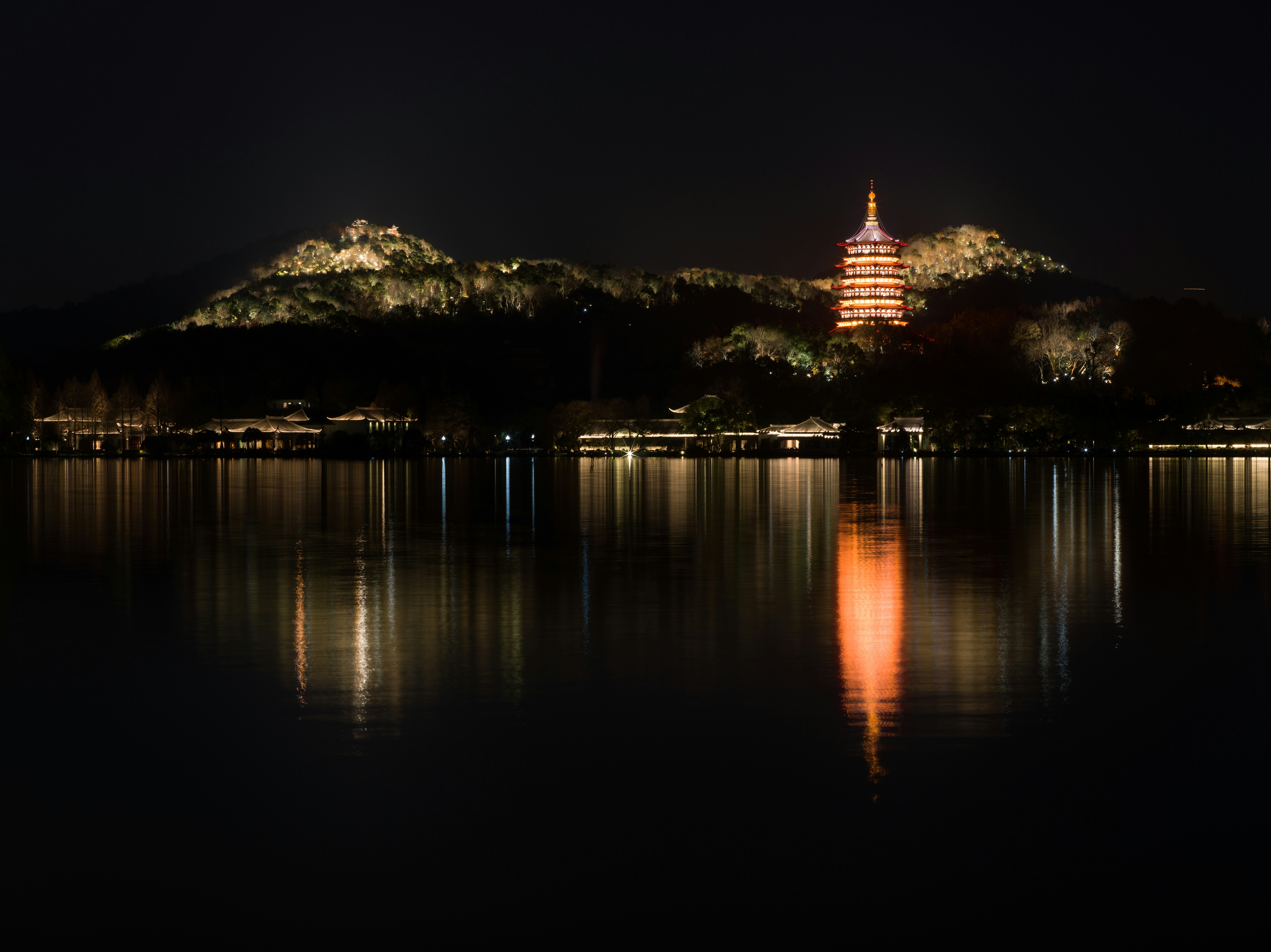 Pagoda and hillside softly illuminated, reflecting on a calm lake under the night sky.