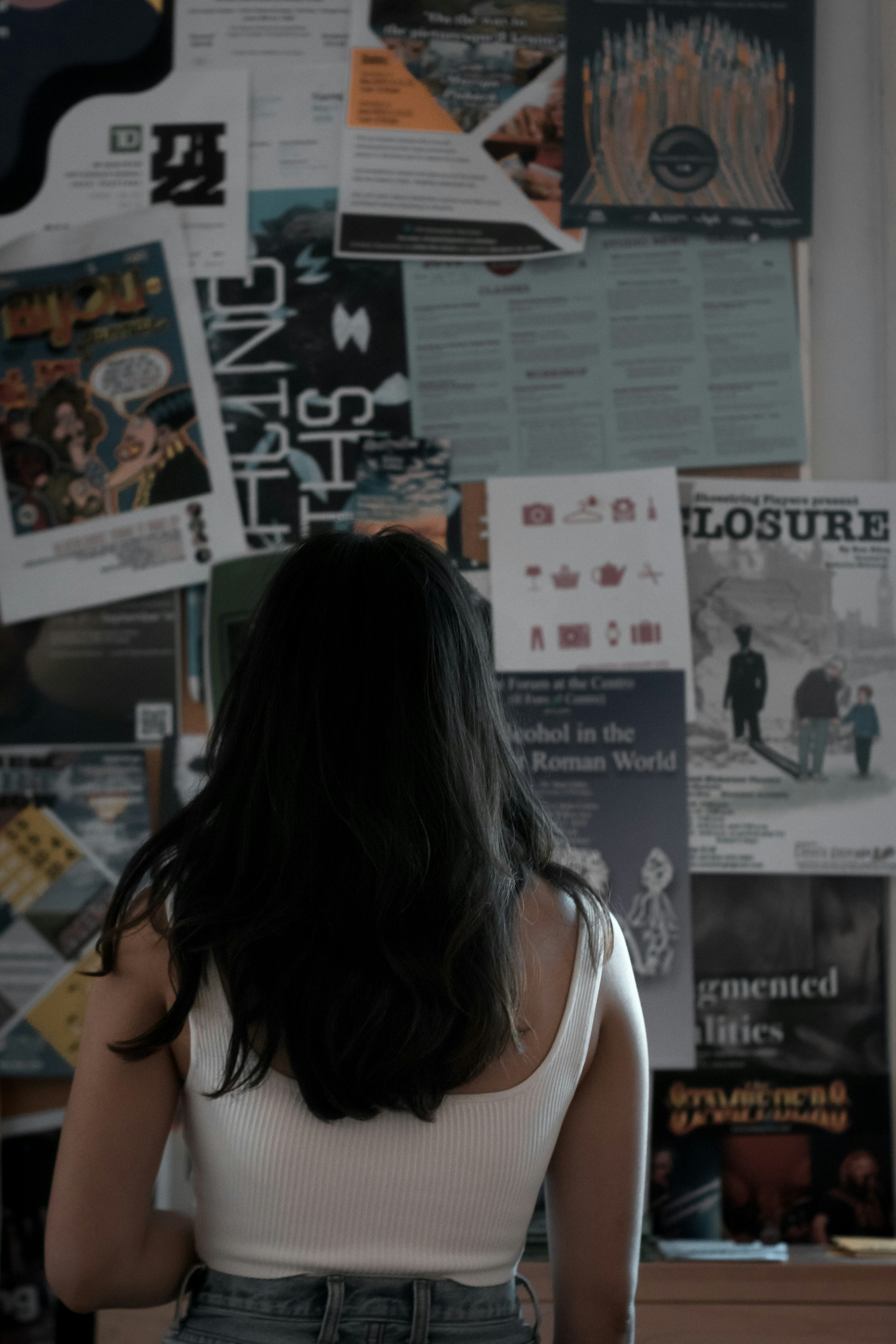 Individual gazing at a collage of posters and flyers on a wall, embodying a vibrant mix of cultural and academic themes.
