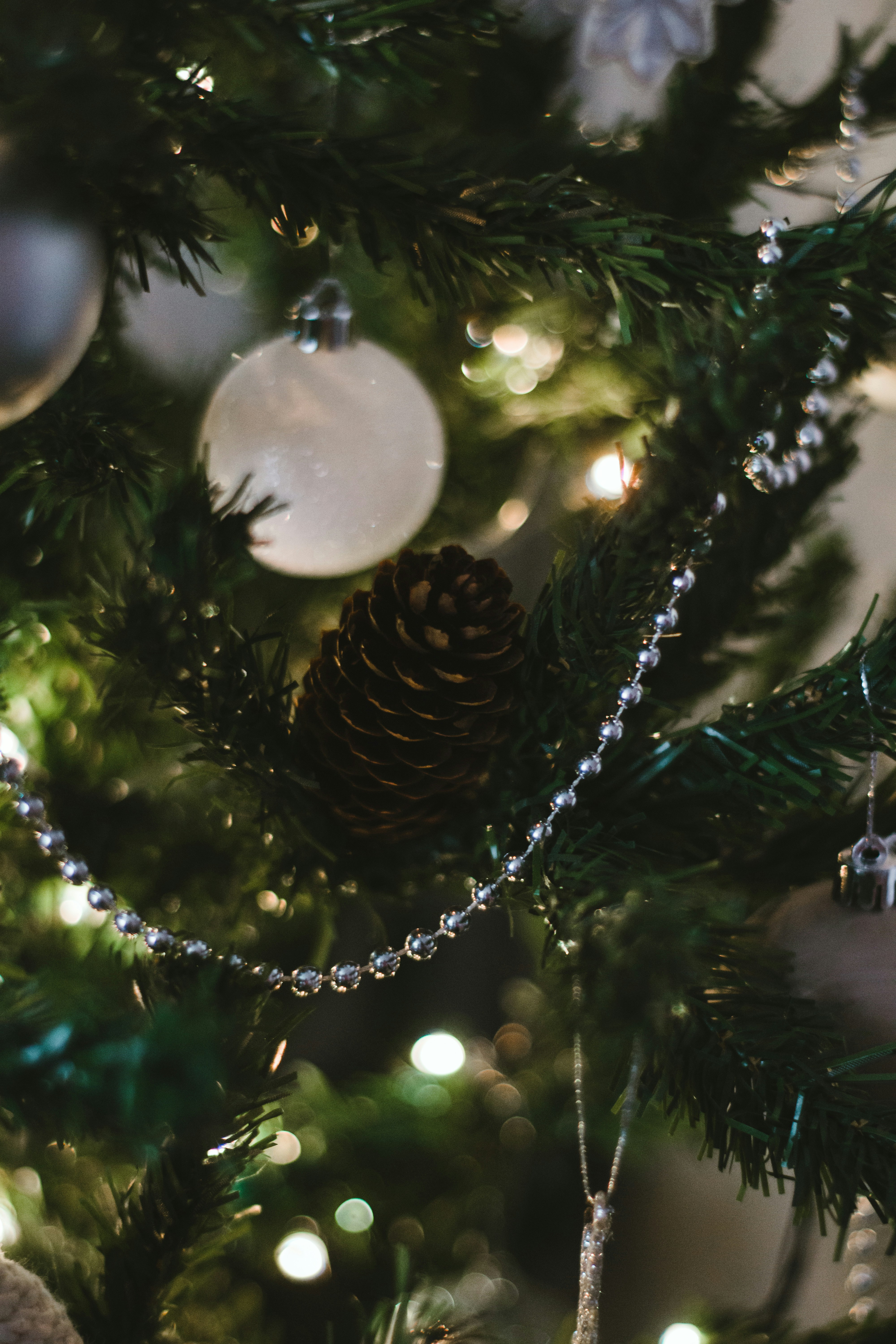 Close-up of a Christmas tree adorned with ornaments, pine cones, and twinkling lights, creating a cozy festive atmosphere.